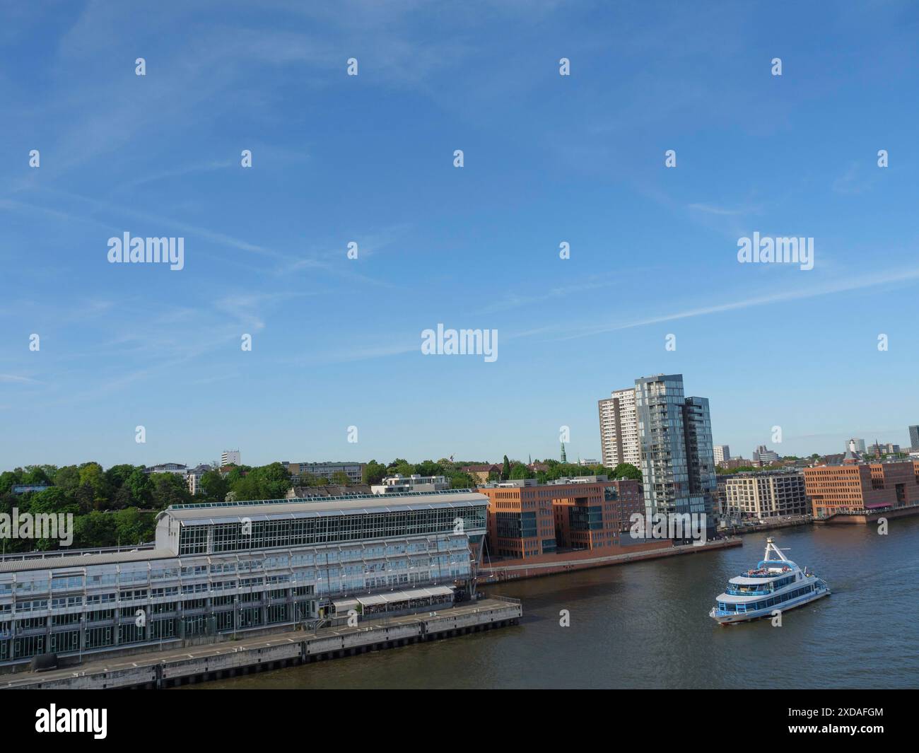 A ship sails past modern harbour buildings under a clear sky with few ...