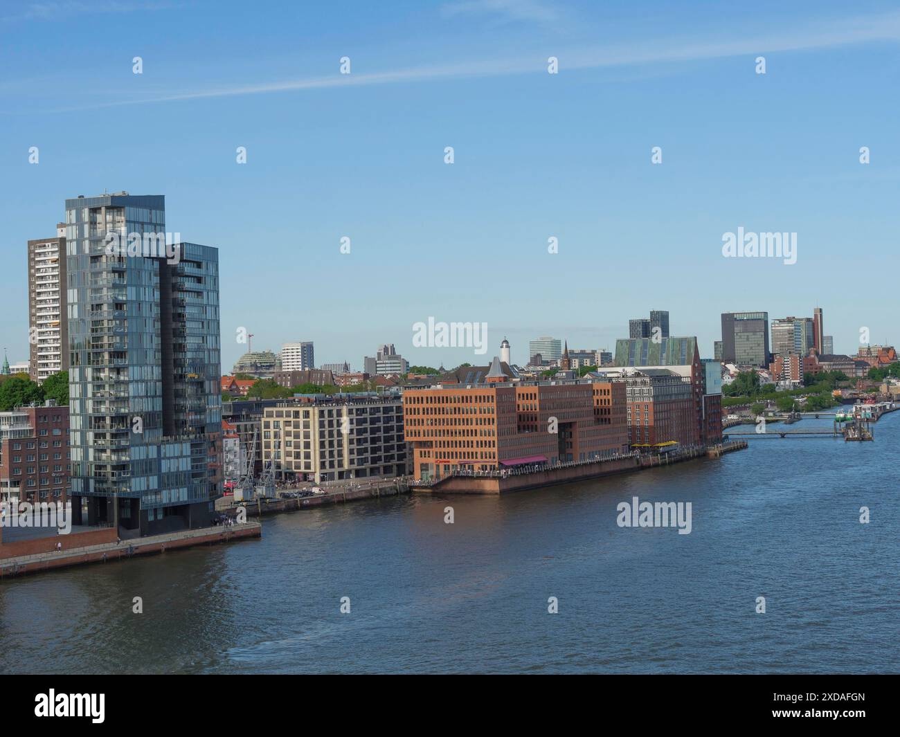 A modern skyscraper next to harbour buildings along a river, showing an ...