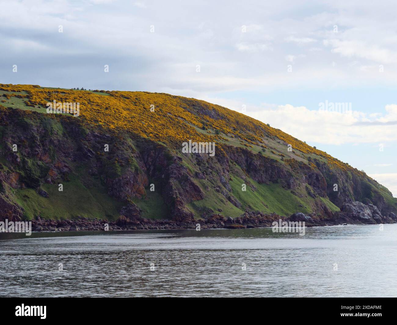 A steep cliff jutting into the calm sea, under an overcast sky with ...