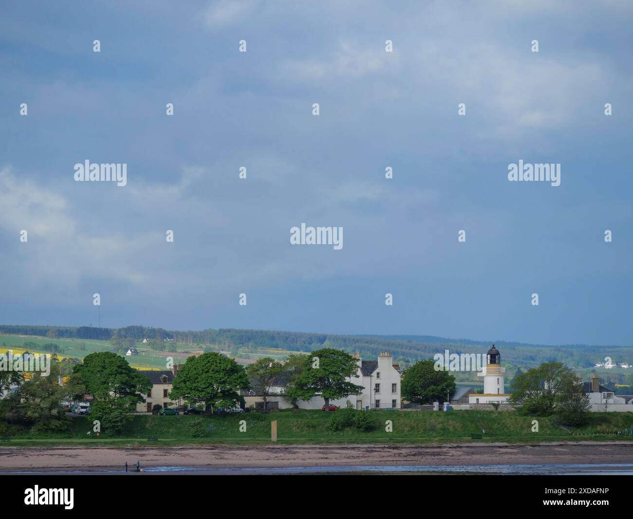 A small village with white houses and tall trees lies against a hilly ...