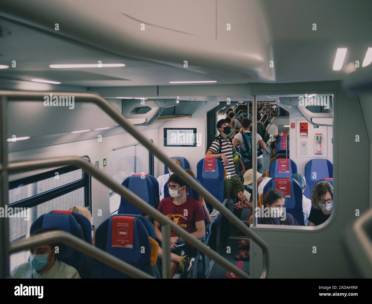 Train interior with passengers seated wearing masks and adhering to ...