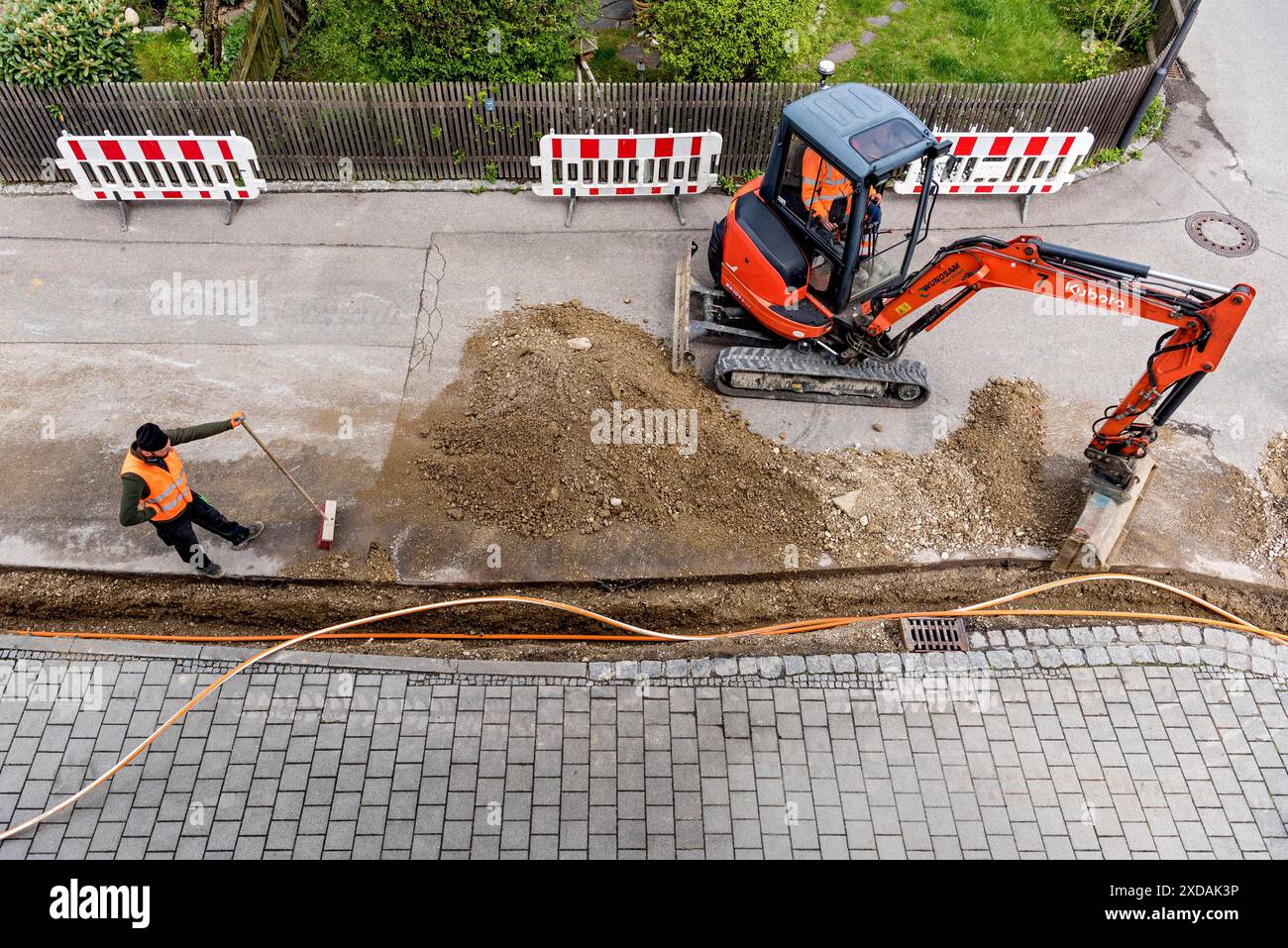 Construction workers lay fibre optic cable in trench under asphalt ...