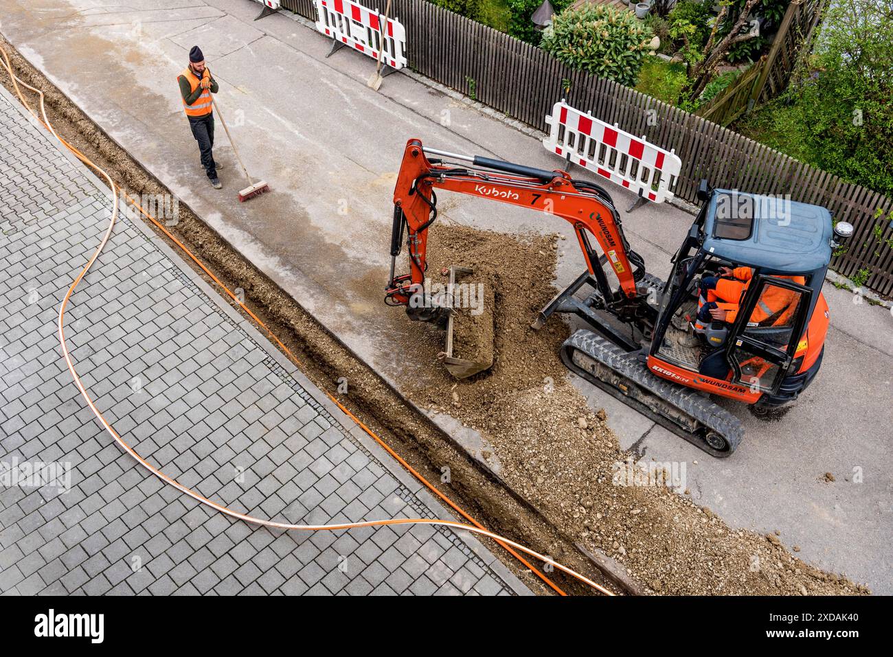 Construction workers lay fibre optic cable in trench under asphalt ...
