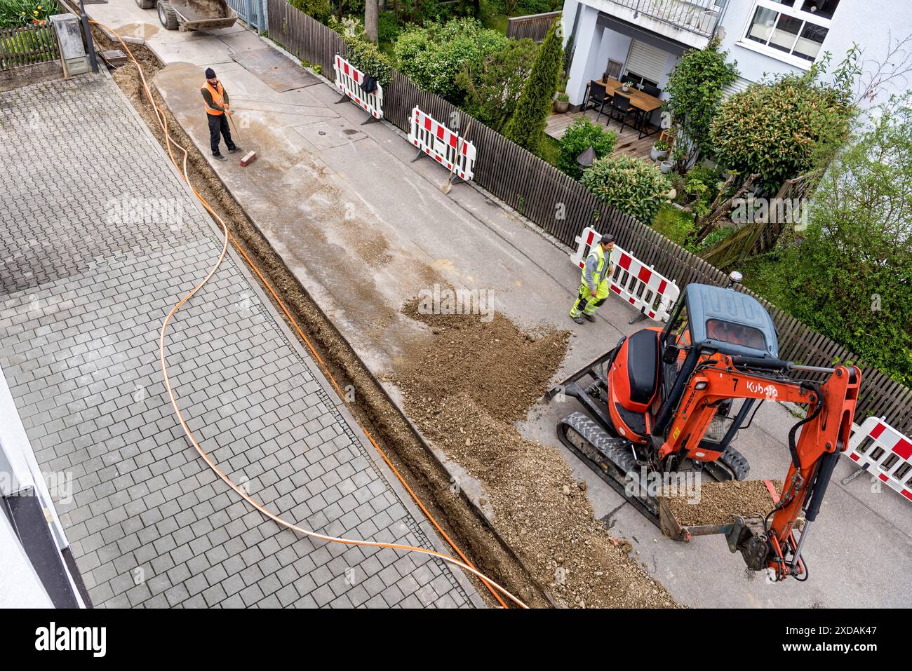 Construction workers lay fibre optic cable in trench under asphalt ...