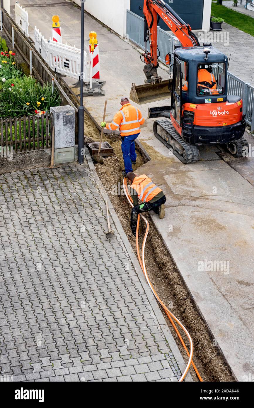 Construction workers lay fibre optic cable in trench under asphalt ...