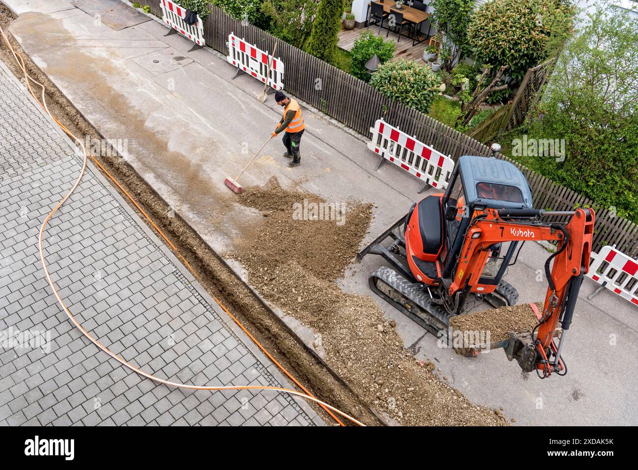 Construction workers lay fibre optic cable in trench under asphalt ...