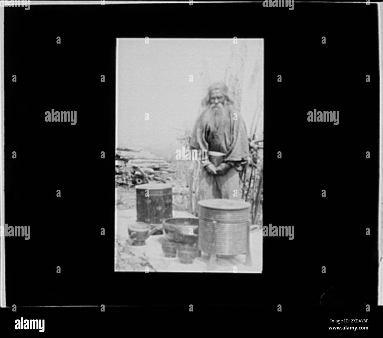 Ainu man standing outdoors on a mat covered with clay containers ...