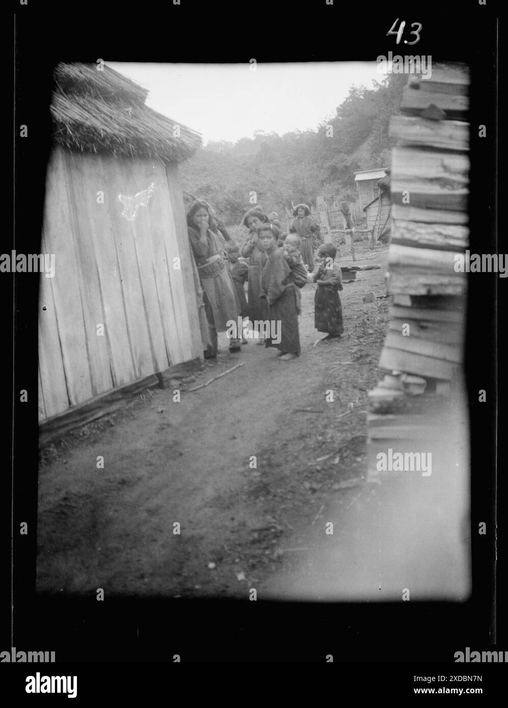 Group of Ainu children standing in a passageway between huts. Genthe ...