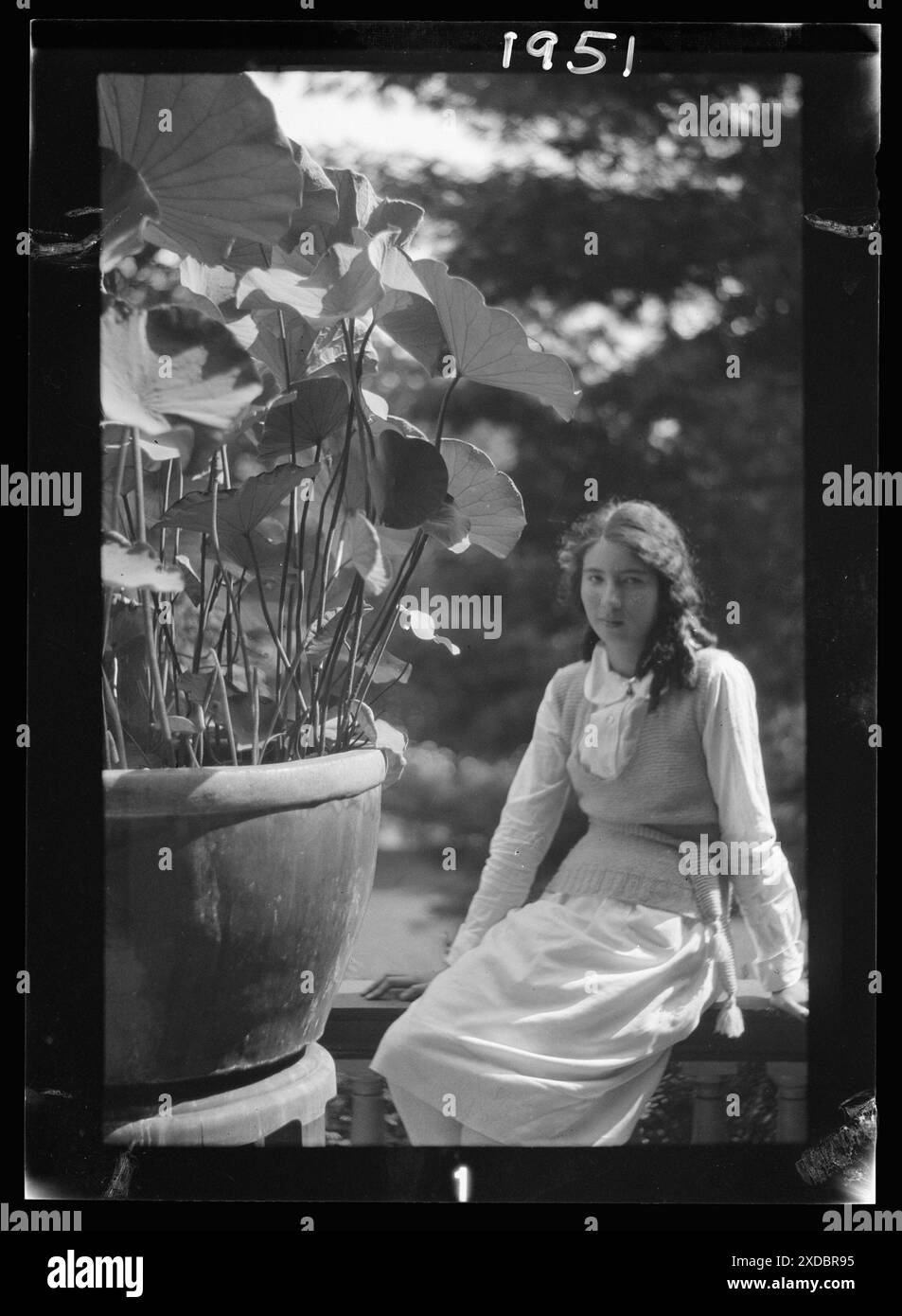 Unidentified woman seated in a garden next to a large potted plant ...
