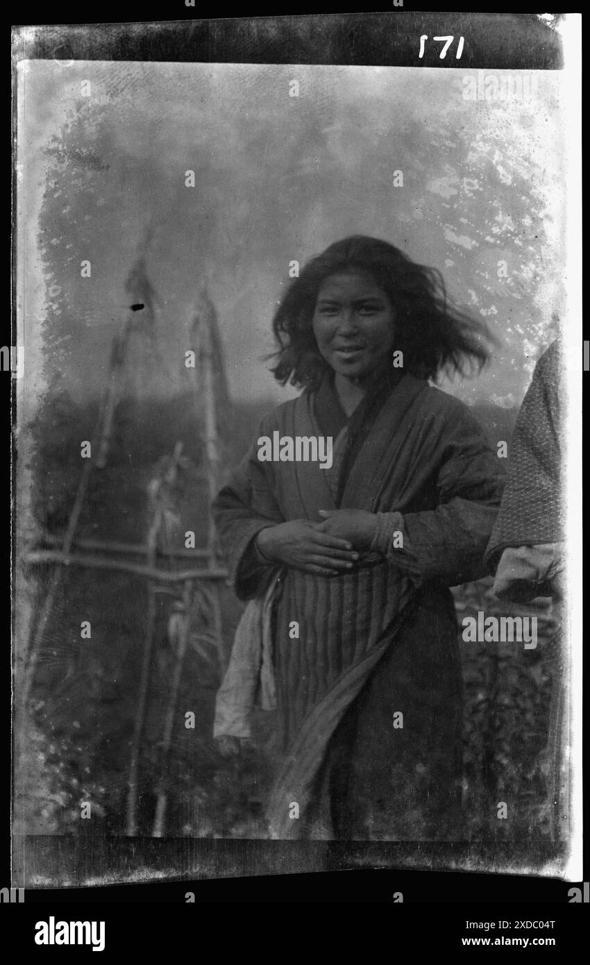 Ainu woman standing outside in front of a pole fence. Genthe photograph ...