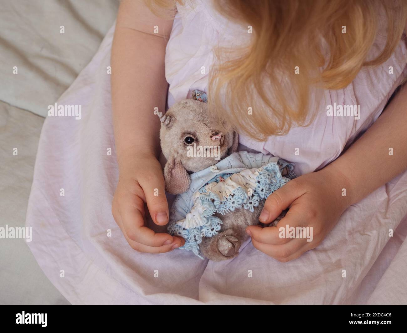 Handcrafted Teddy Lamb in Blonde Toddler Girl’s Hands Against a Pastel Pink Cotton Dress ...