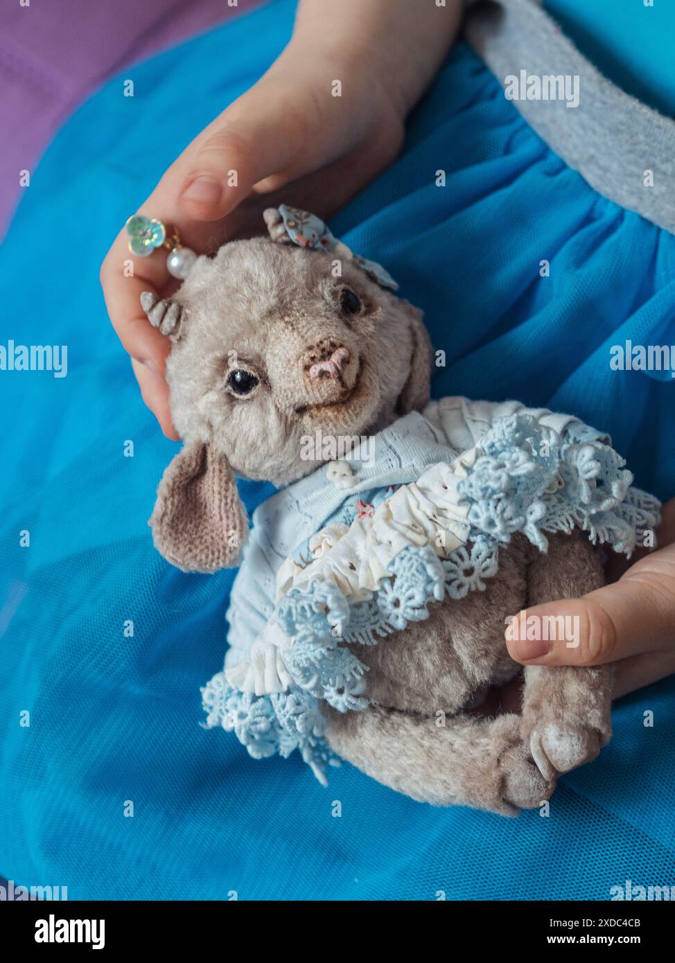 Teddy Lamb in Toddler’s Hands Against a Vibrant Blue Tulle Dress Backdrop. A vertical close up ...