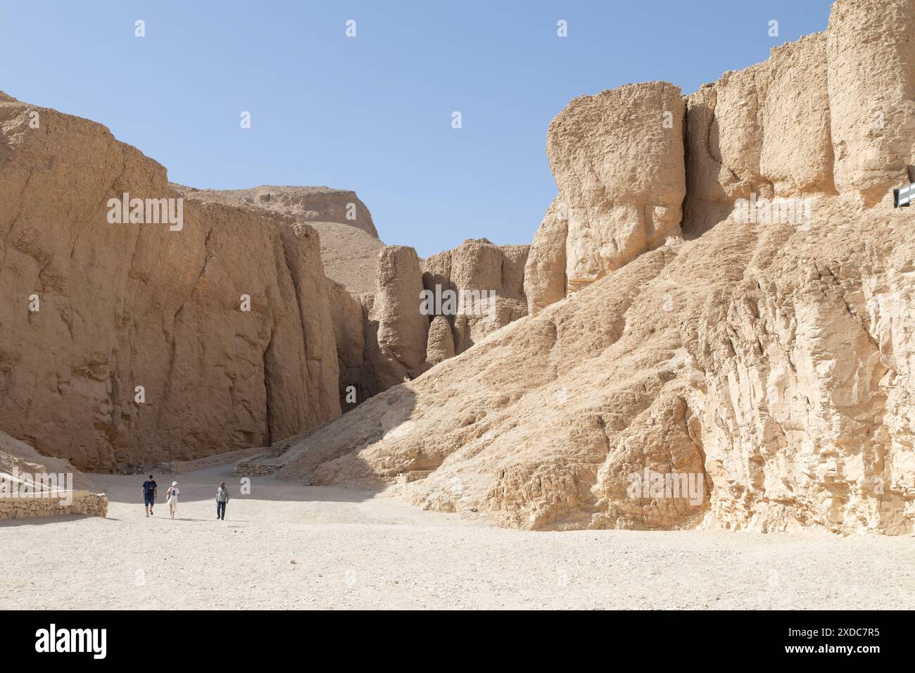 Three people in modern dress are dwarfed by the arid limestone cliffs ...