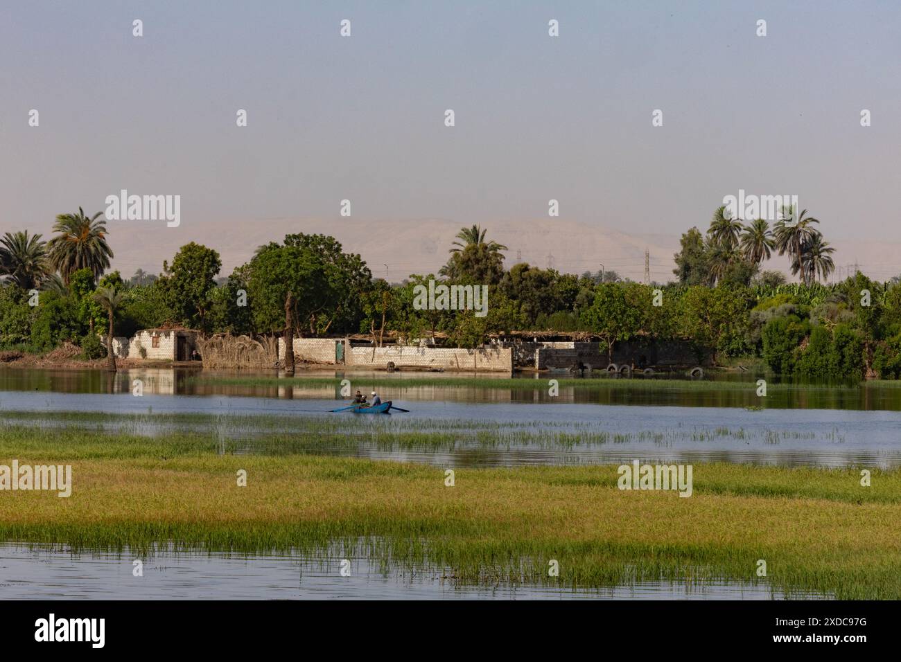 Two Egyptians row a wooden boat on the mirror-like surface of the Nile ...