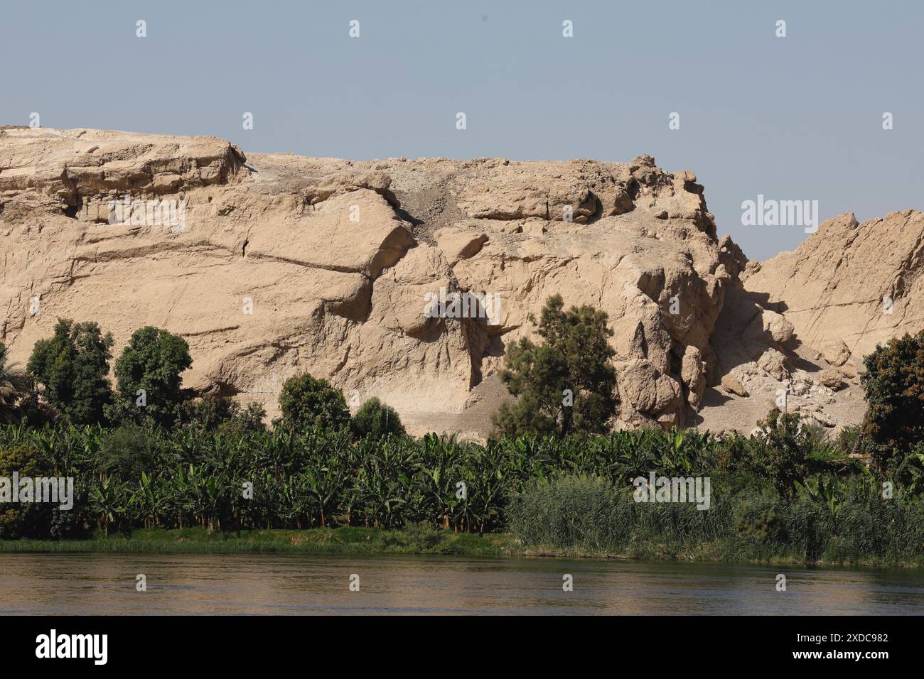Arid sandstone cliffs with a narrow fringe of greenery at their base ...