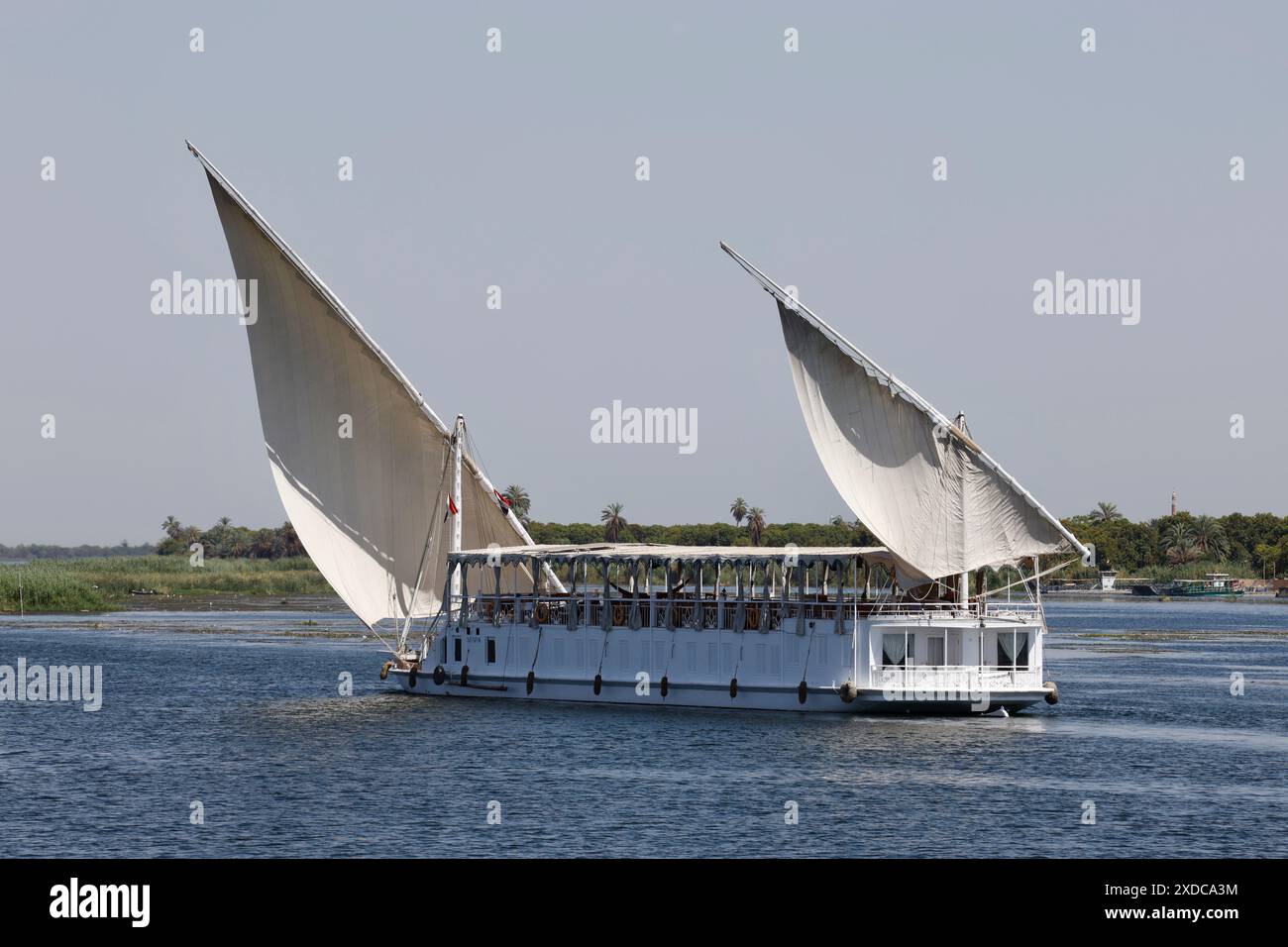 The "Minya" dahabiya two-masted sailing boat with latin-rig white sails cruises quietly down the ...