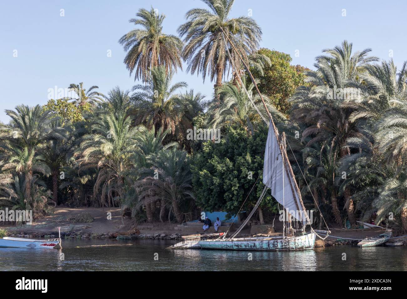 Three Egyptians sit on a bench in he shade by the Nile in front of a ...