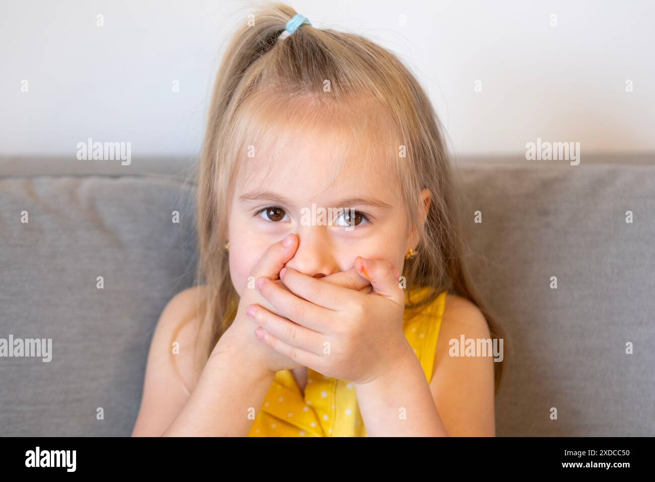 sweet child, shy blonde girl covered mouth with hands, struggle to keep secret and maintain self ...