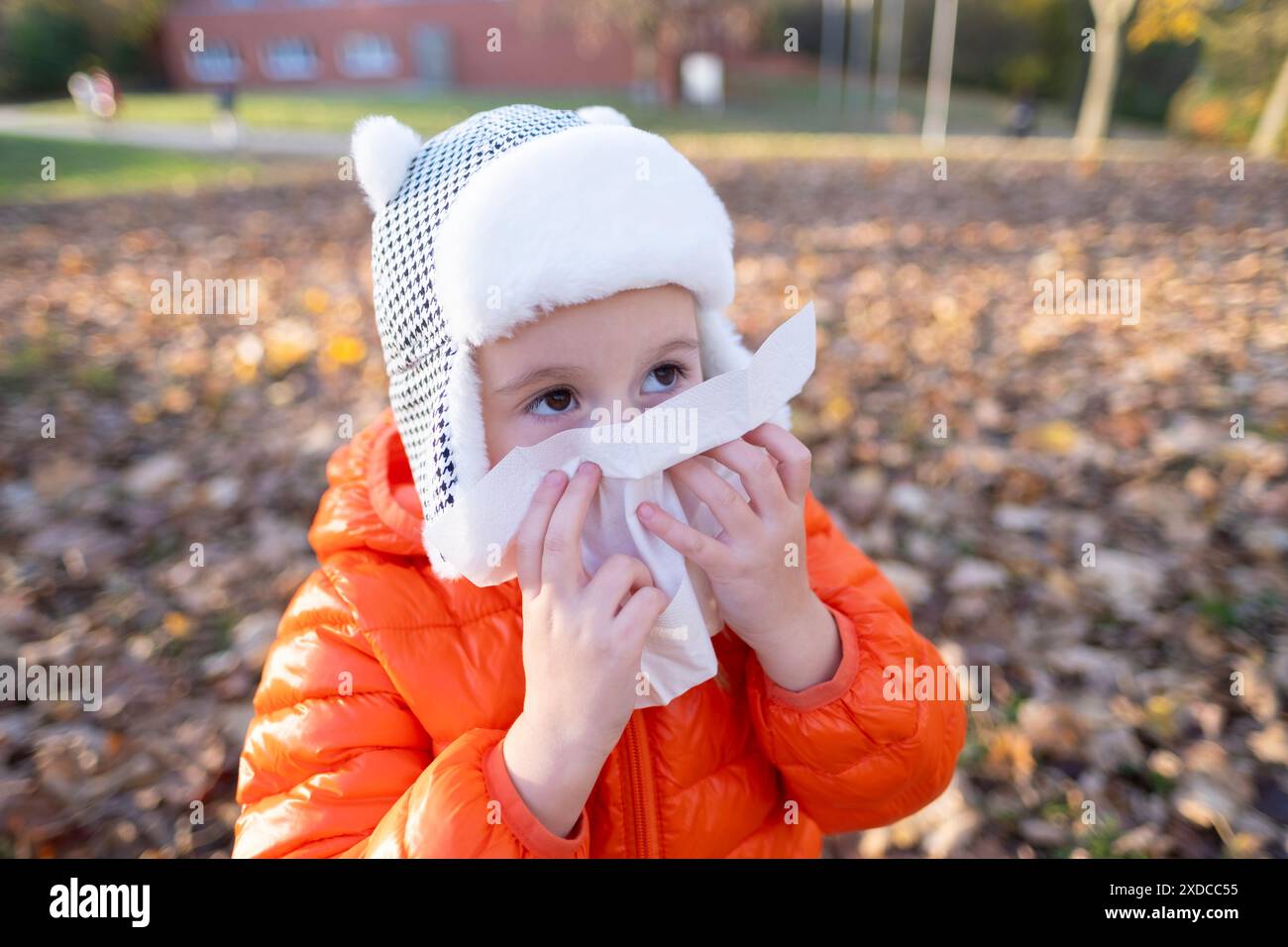 runny nose in child, girl in orange jacket blows nose into paper napkin ...