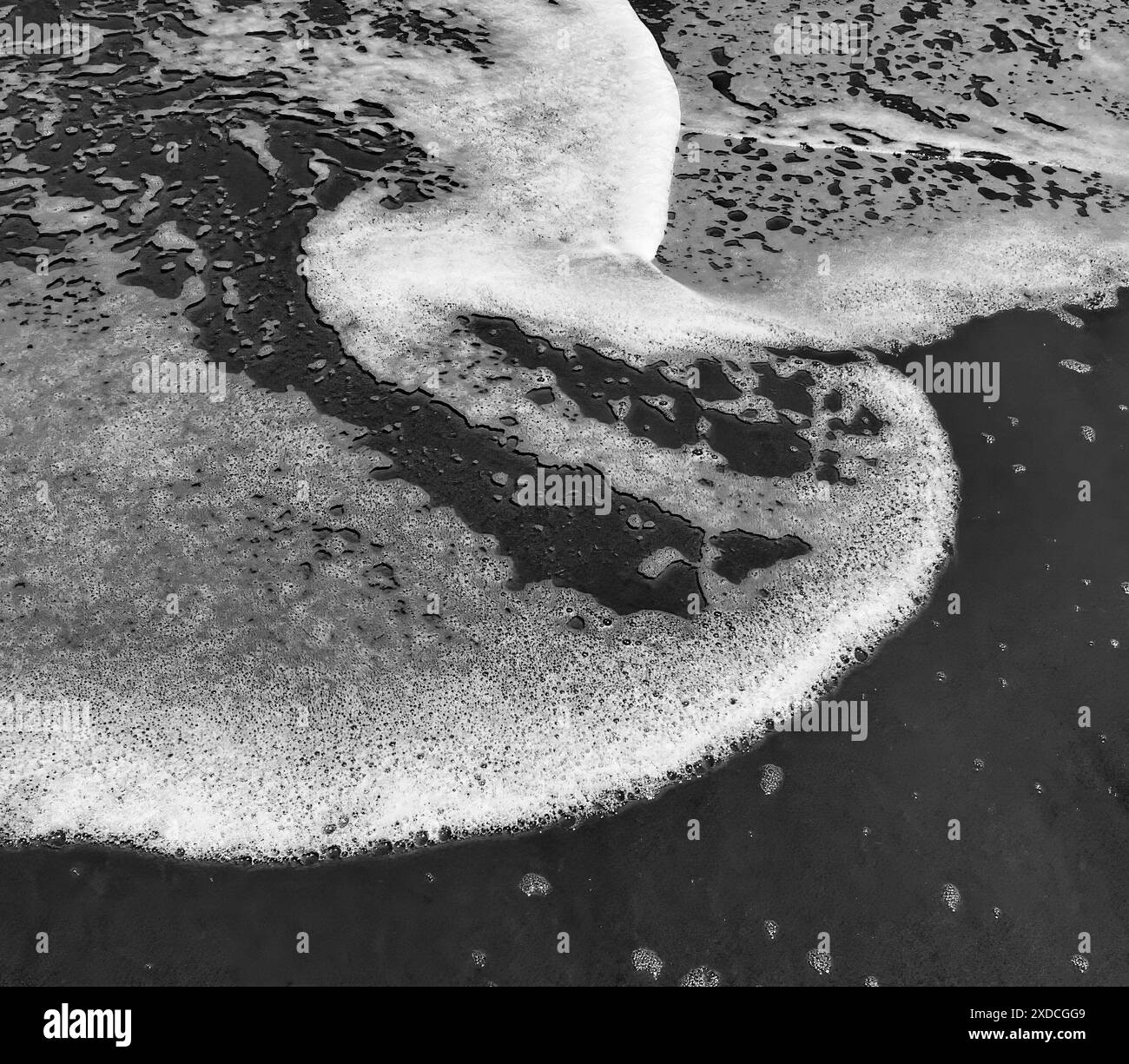 A black and white photograph depicting the receding foamy waves of the ...