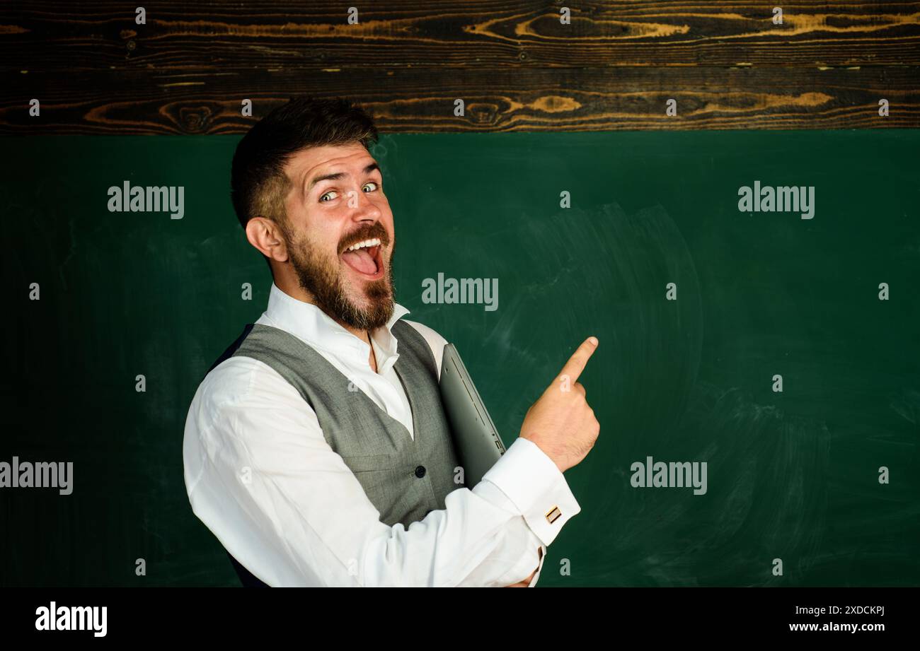 Happy bearded teacher or student with laptop pointing finger at ...