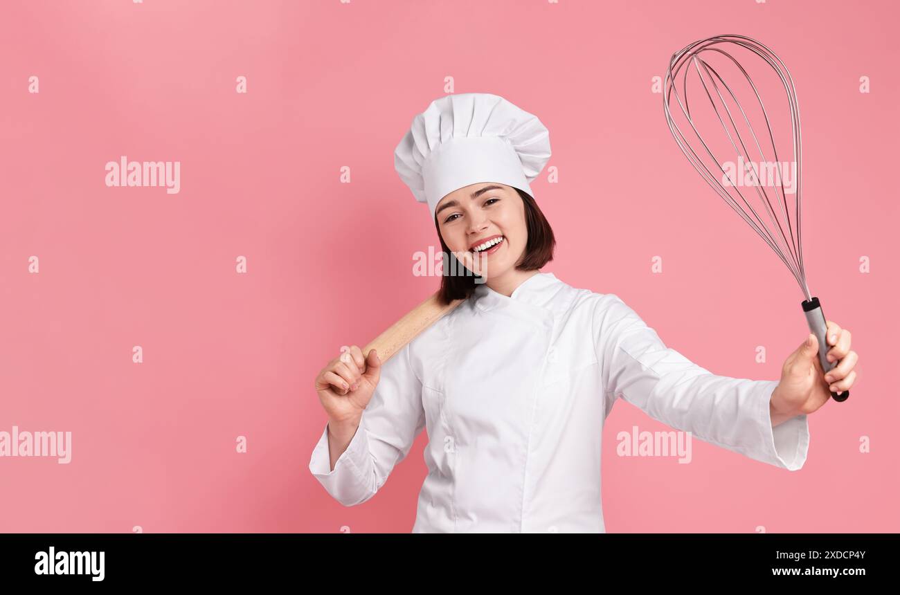 Happy pastry chef with big whisk and rolling pin on pink background ...