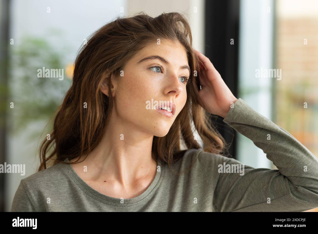 Woman with long hair touching her head, gazing thoughtfully Stock Photo ...