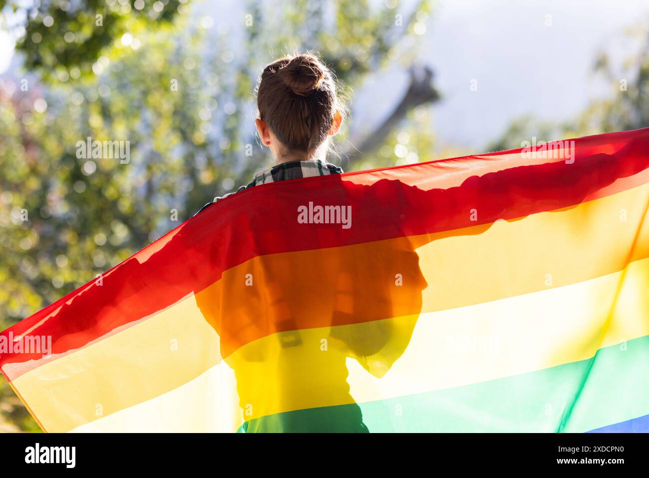 Woman holding rainbow flag draped over shoulders, standing outside ...