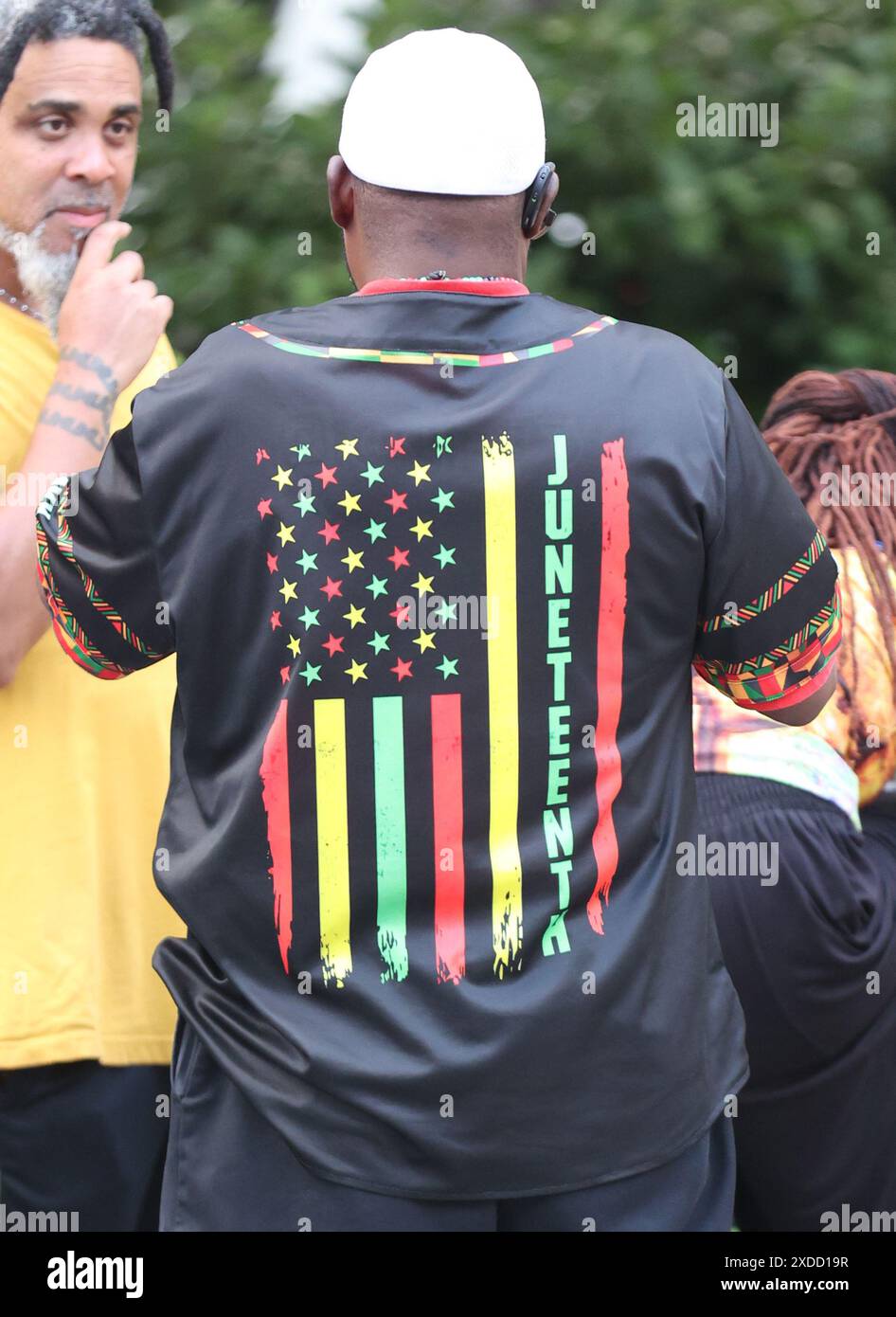 A man sporting a Juneteenth baseball jersey talks to an event goer ...