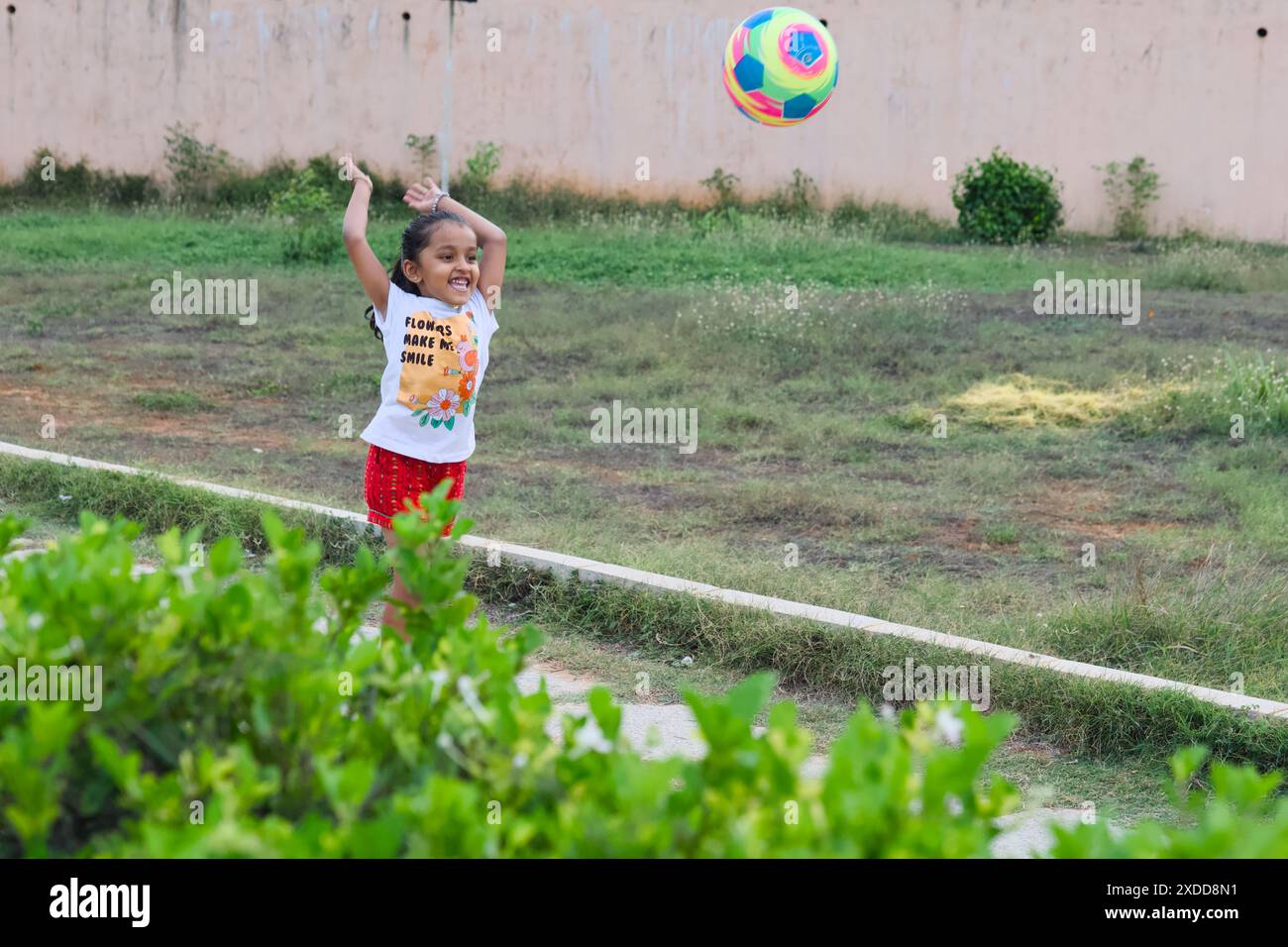 A young kid gleefully tosses a vibrant ball outdoors, capturing the ...