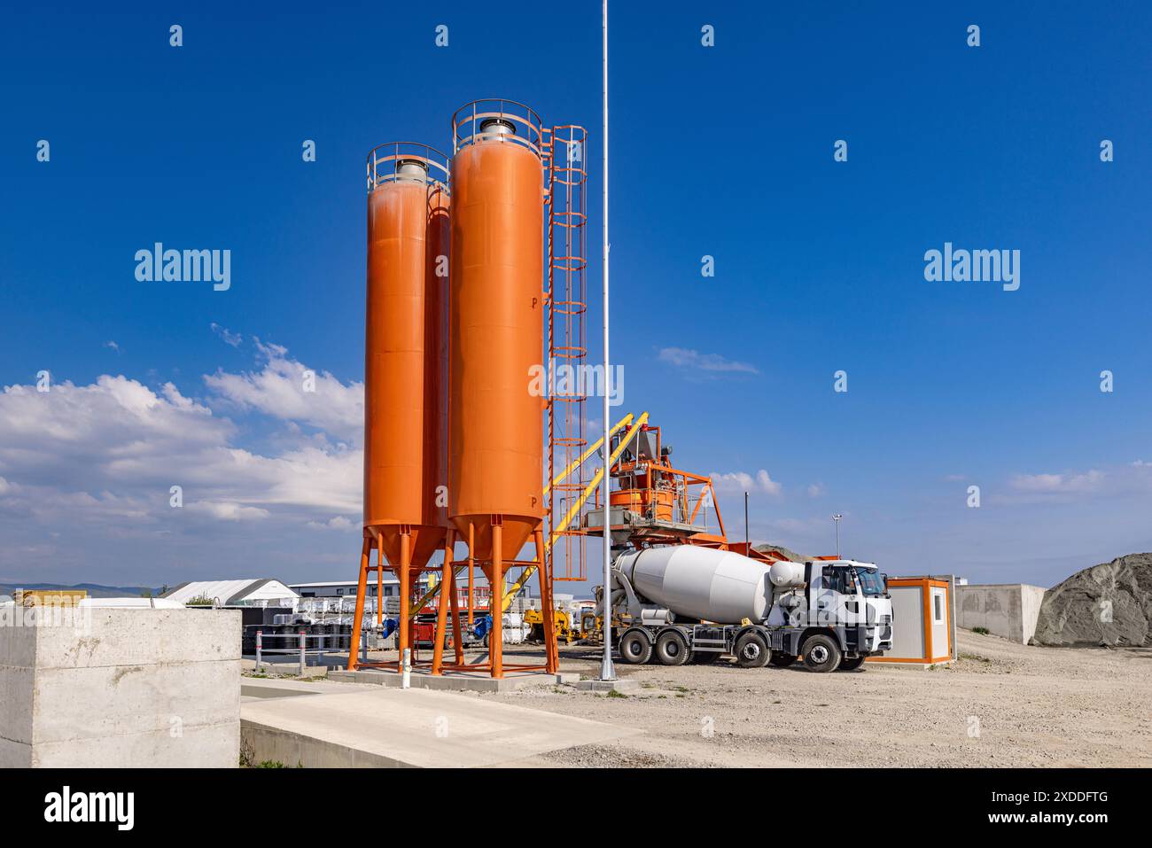 Orange industrial cement plant with storage silos, surrounded by a concrete ground against a ...