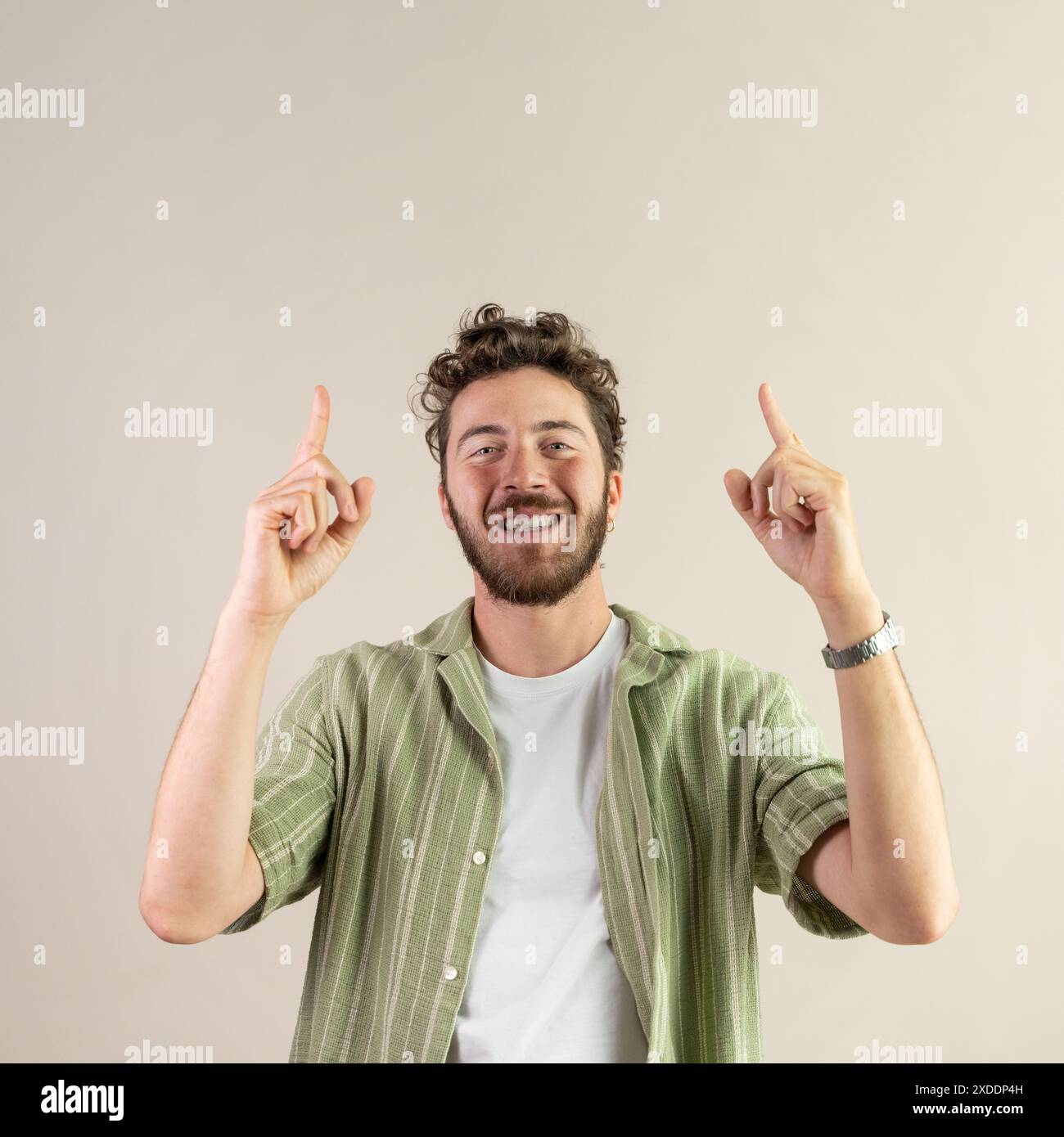 A young man in a green shirt pointing upwards with both hands, smiling ...