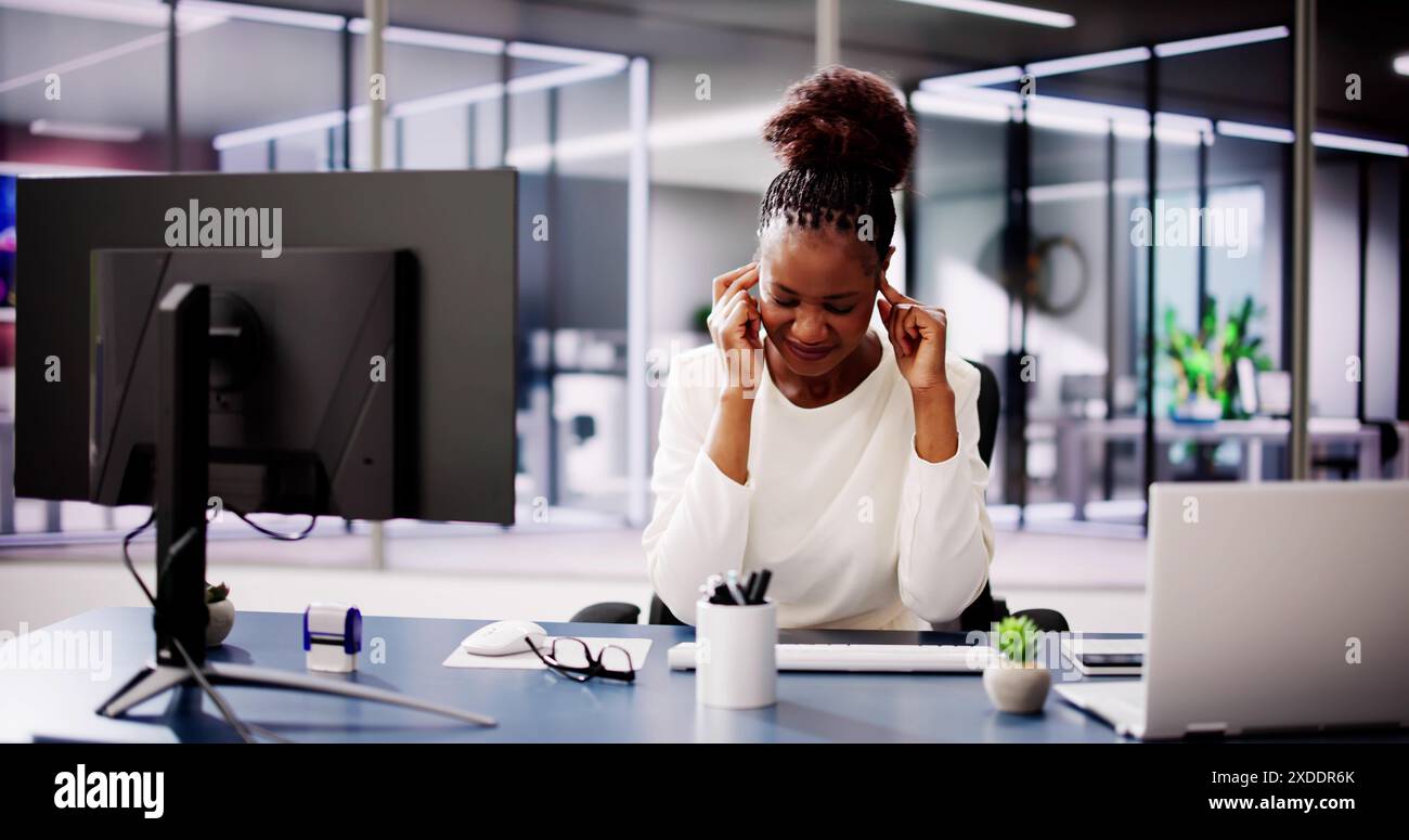 Focused black woman with hand covering ear, trying to hear over loud ...