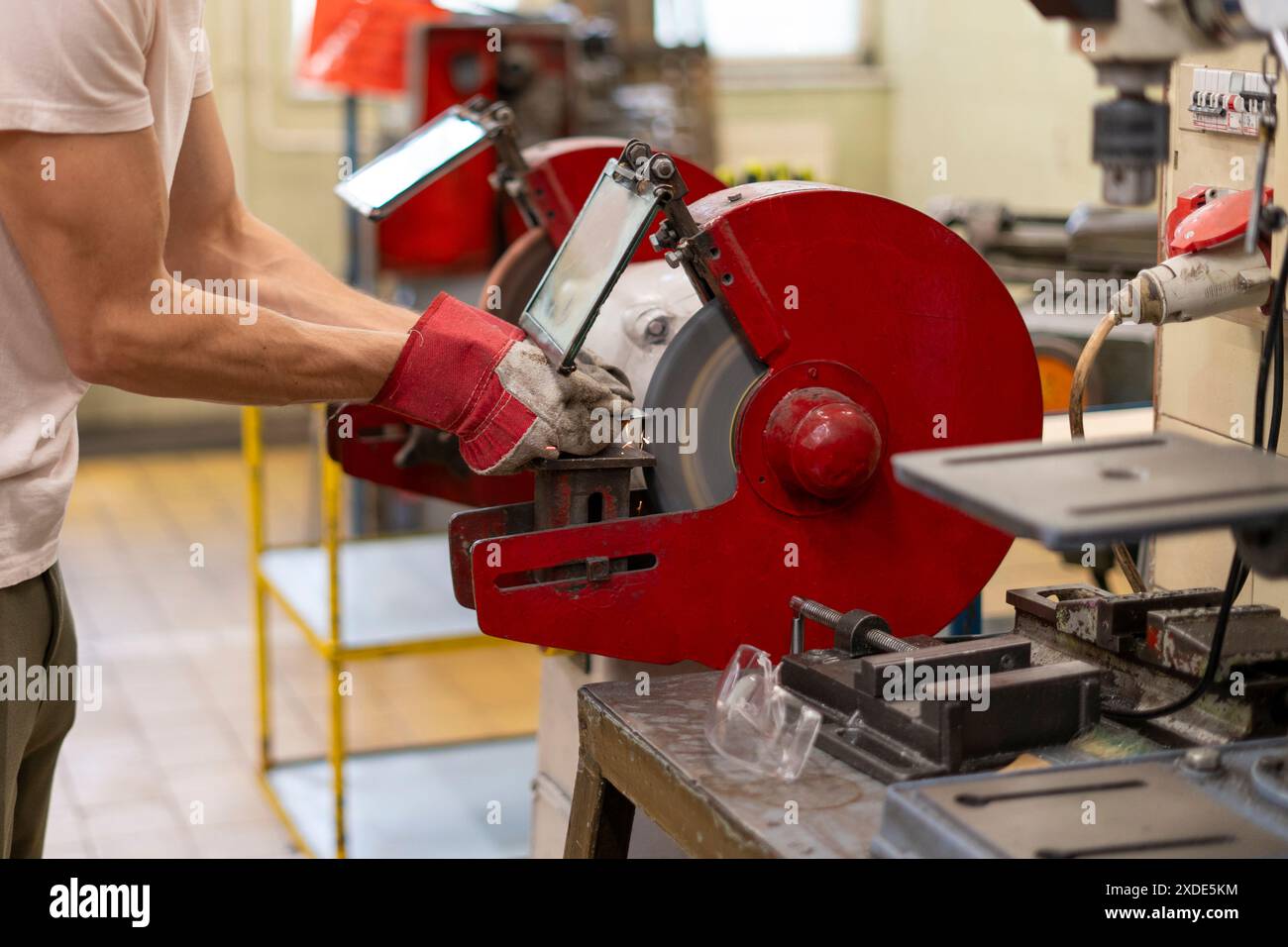 A worker grinding a tool on a red grinding machine in a workshop Stock ...