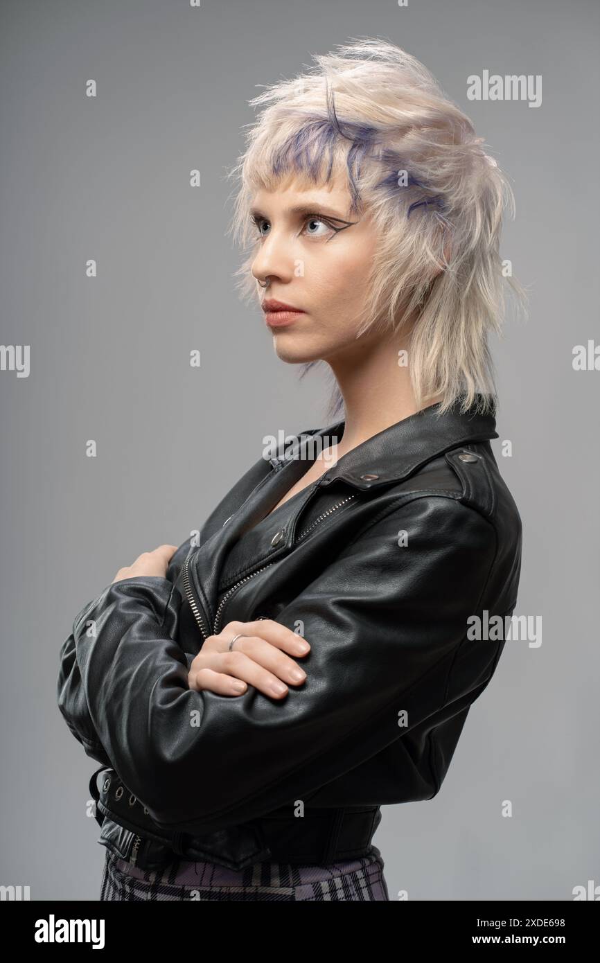 A young woman with a modern hairstyle wearing a leather jacket, arms ...
