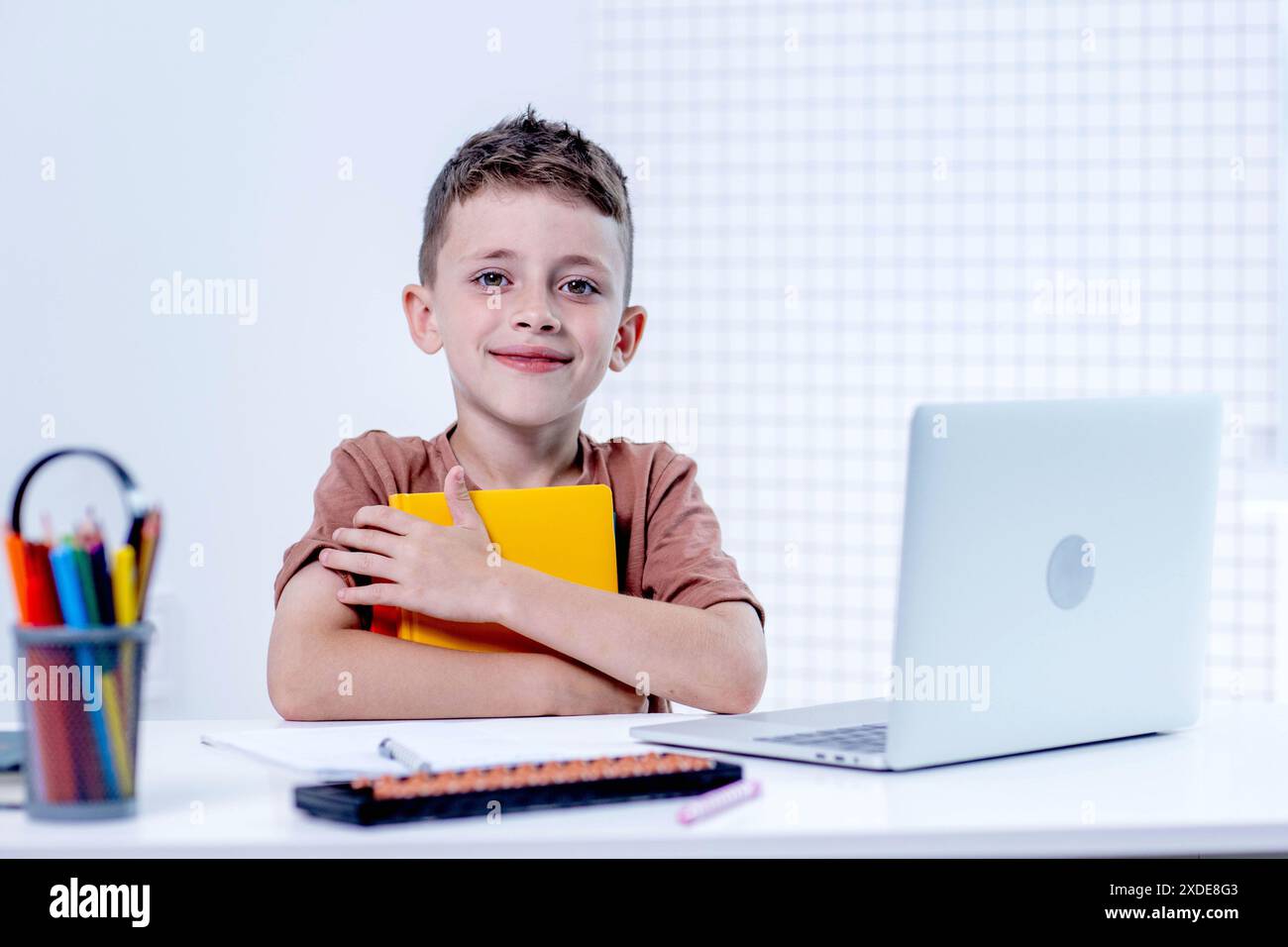 Smart schoolboy is ready to study at a neat table in a white interior ...