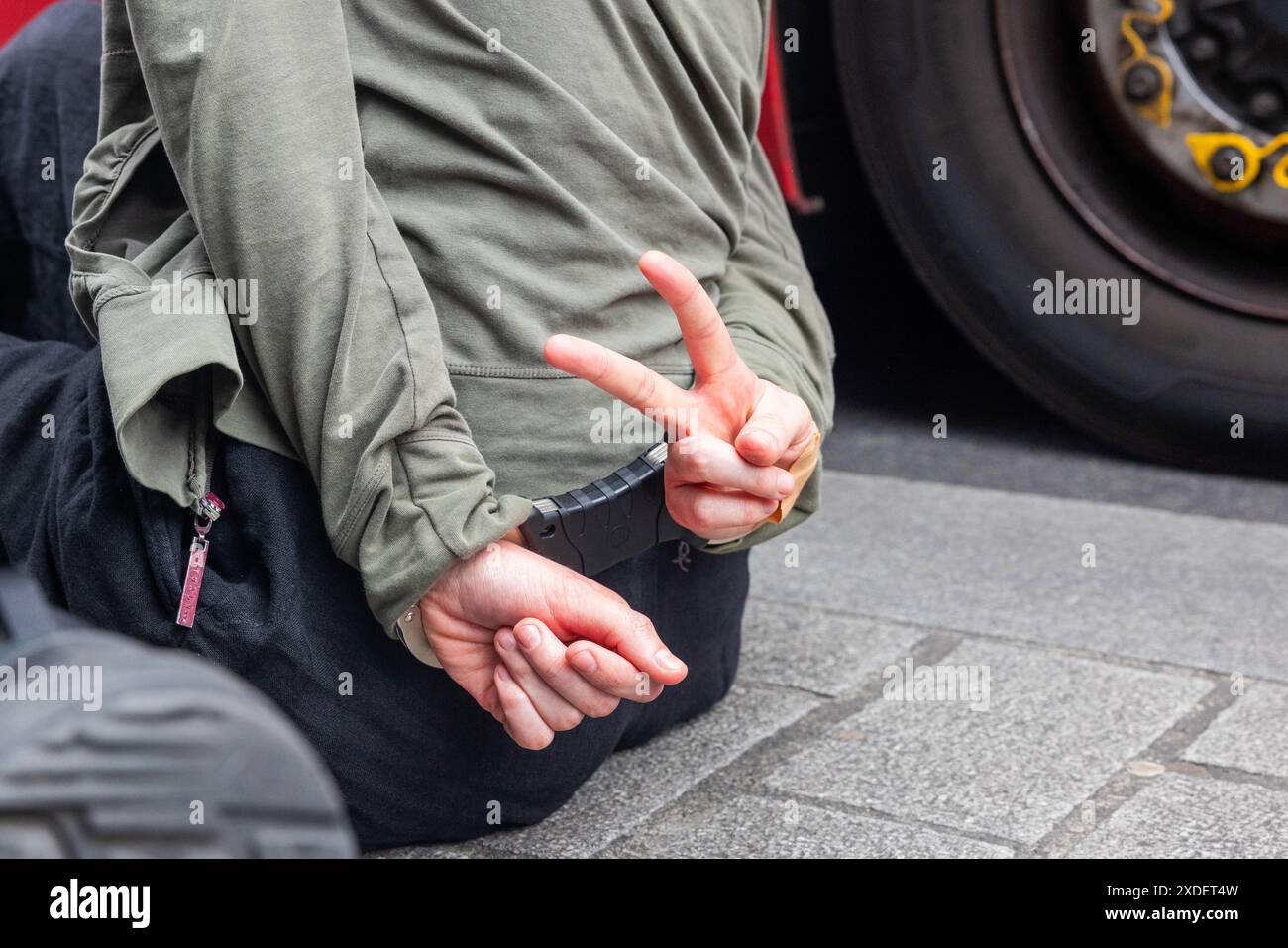 London, UK. 22 JUN, 2024. Protestor in handcuffs raises peace sign as ...