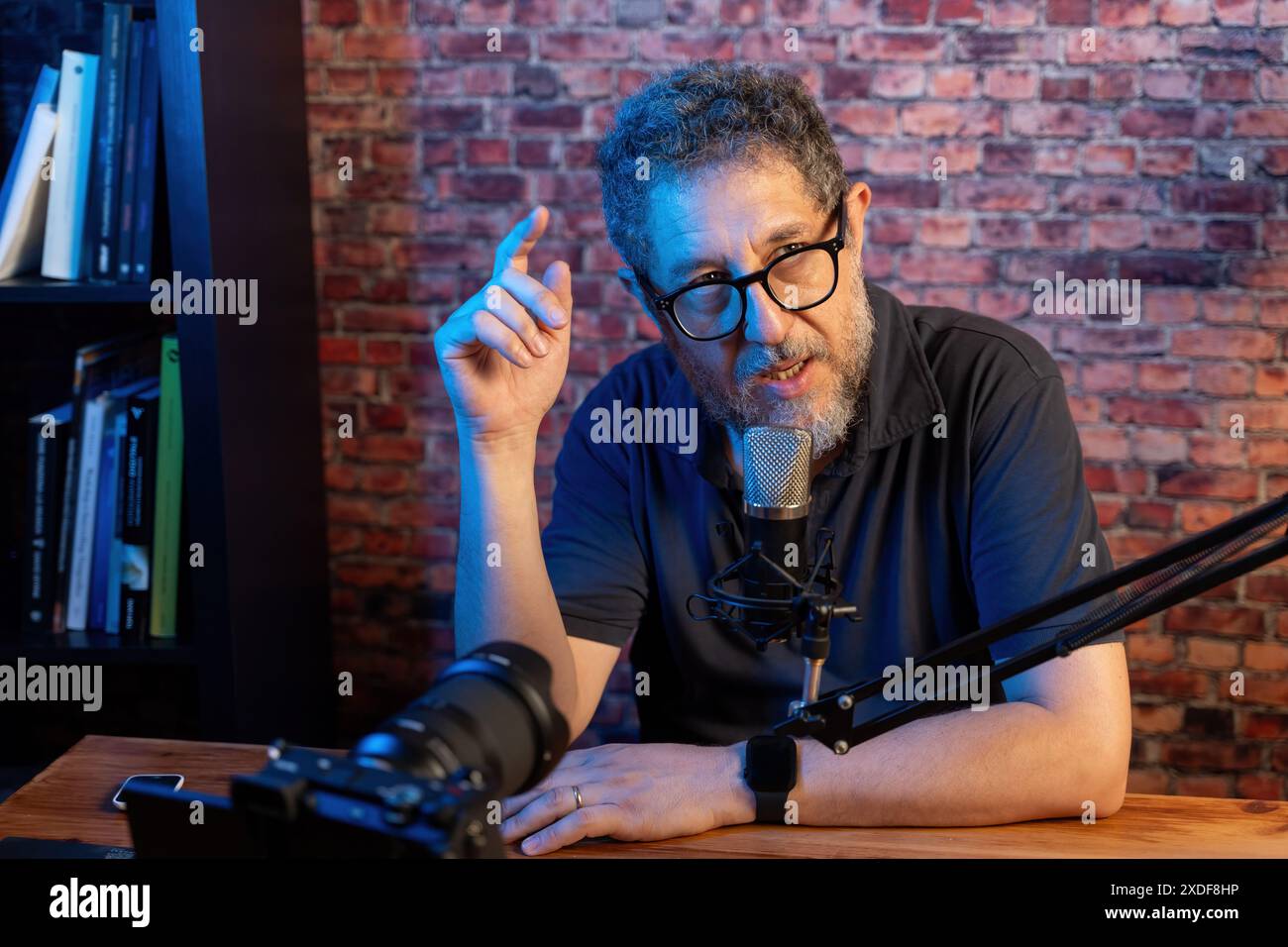A middle-aged man with glasses and a beard podcasting with a microphone ...