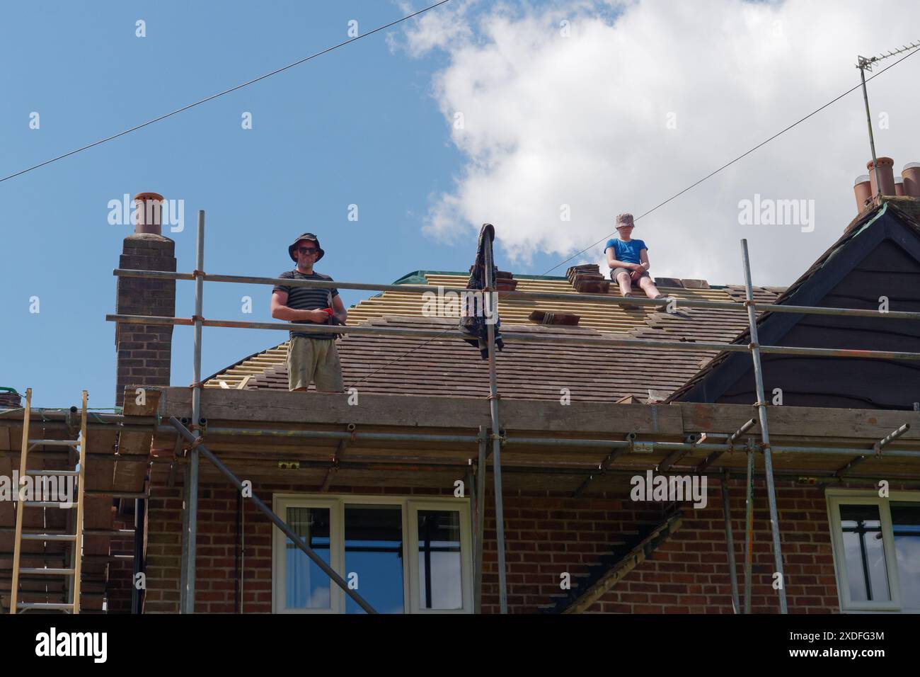 Father and son pause during roof repair work with ladder and ...