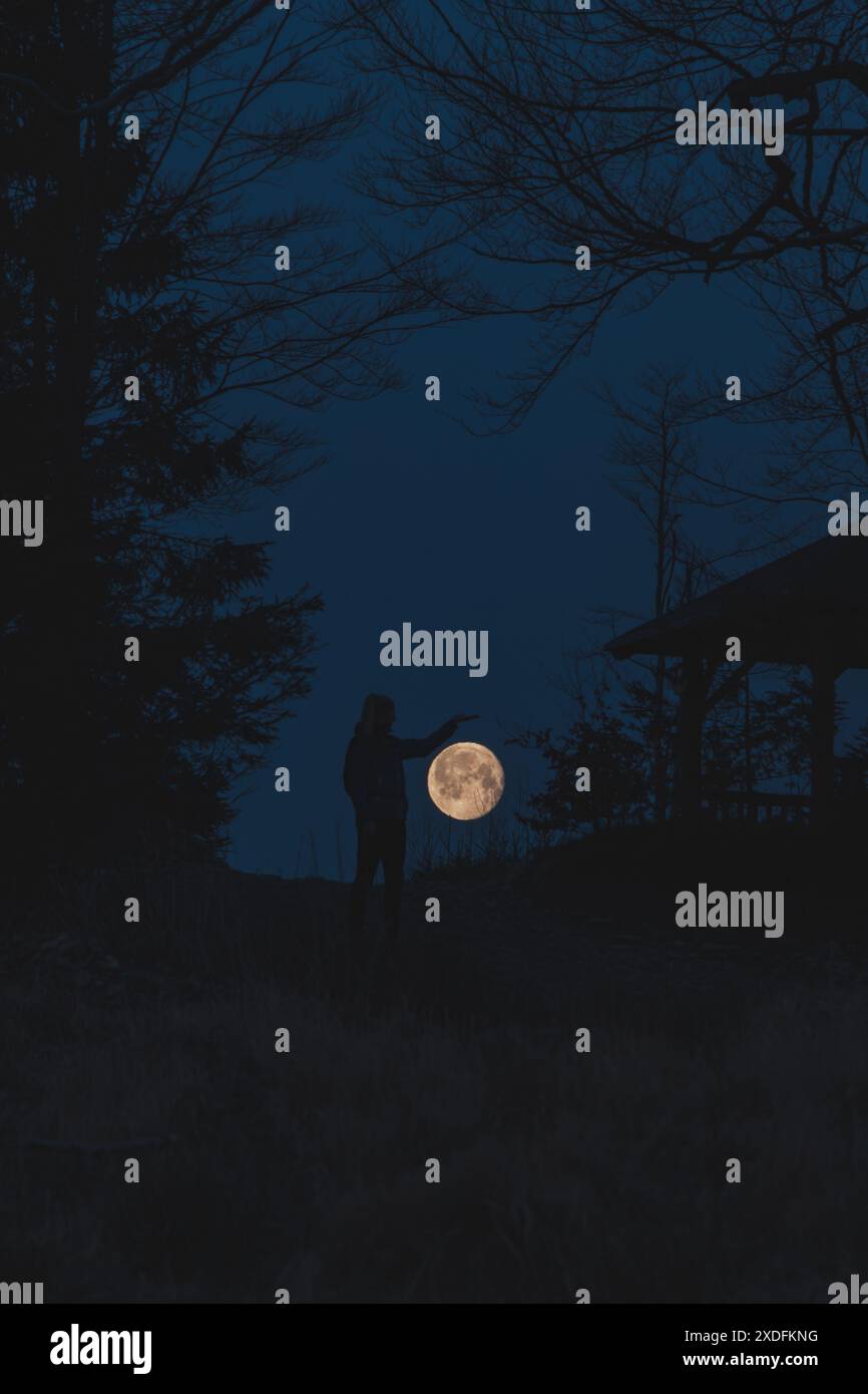 Silhouette of a figure holding the full moon on a mountainside. The ...