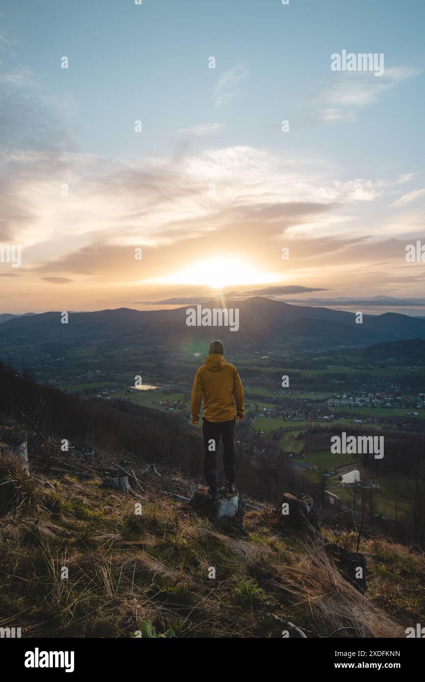Adventurous man standing on a tree stump and observing the sunrise in ...