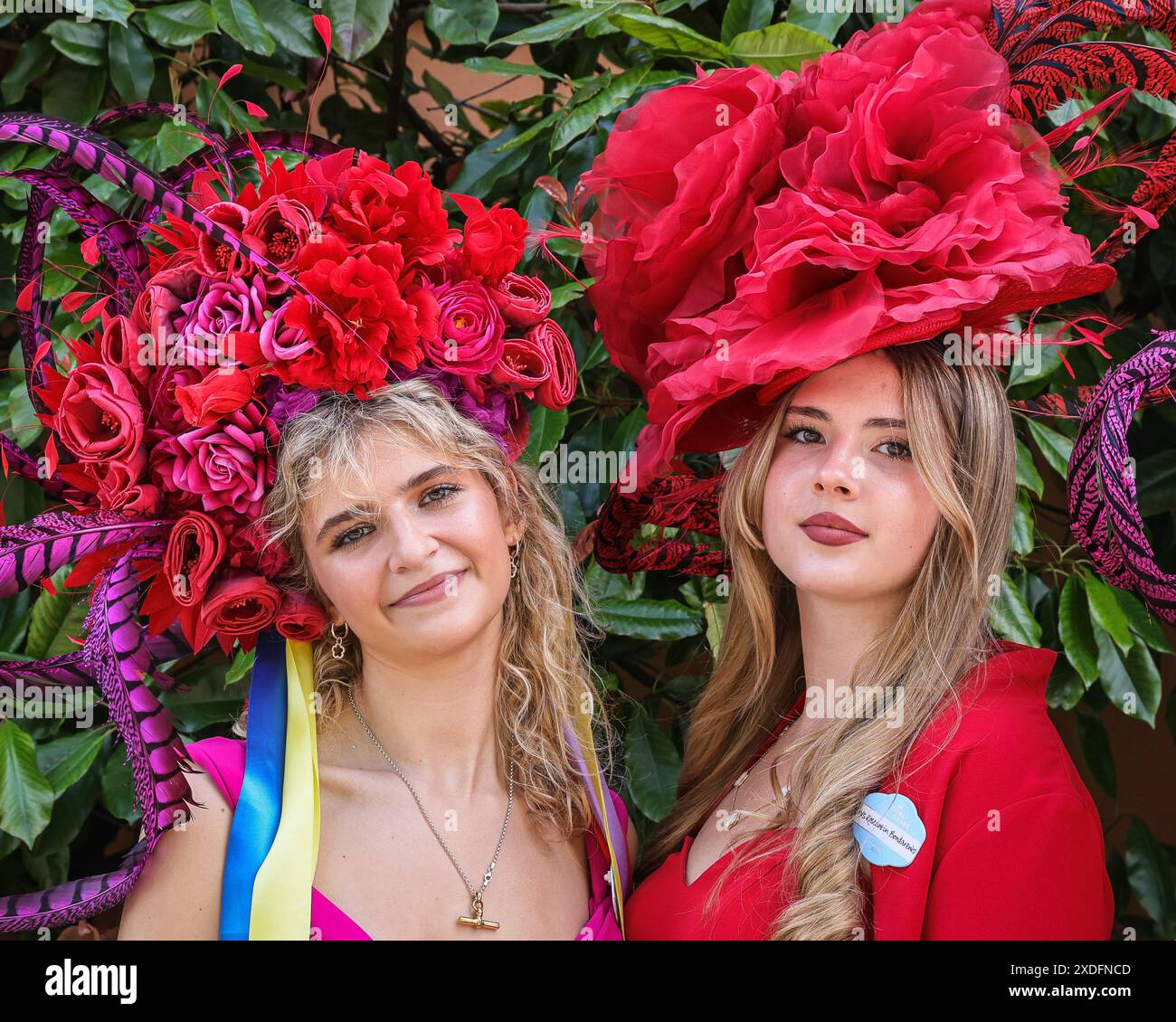 Two young ladies in dresses and elaborate red rose hats pose and smile ...