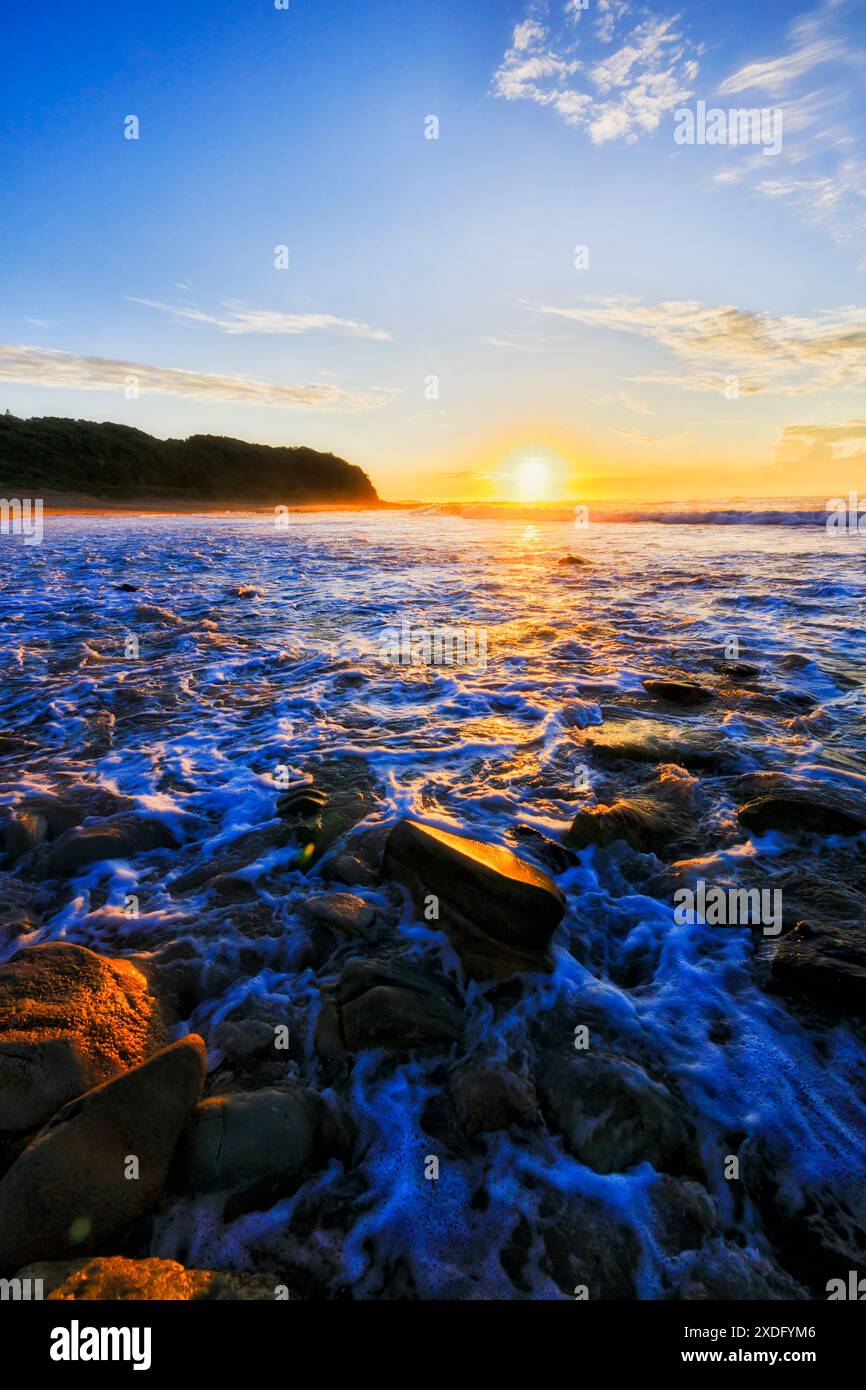Bright rising sun over Pacific ocean horizon at Caves beach coastal ...