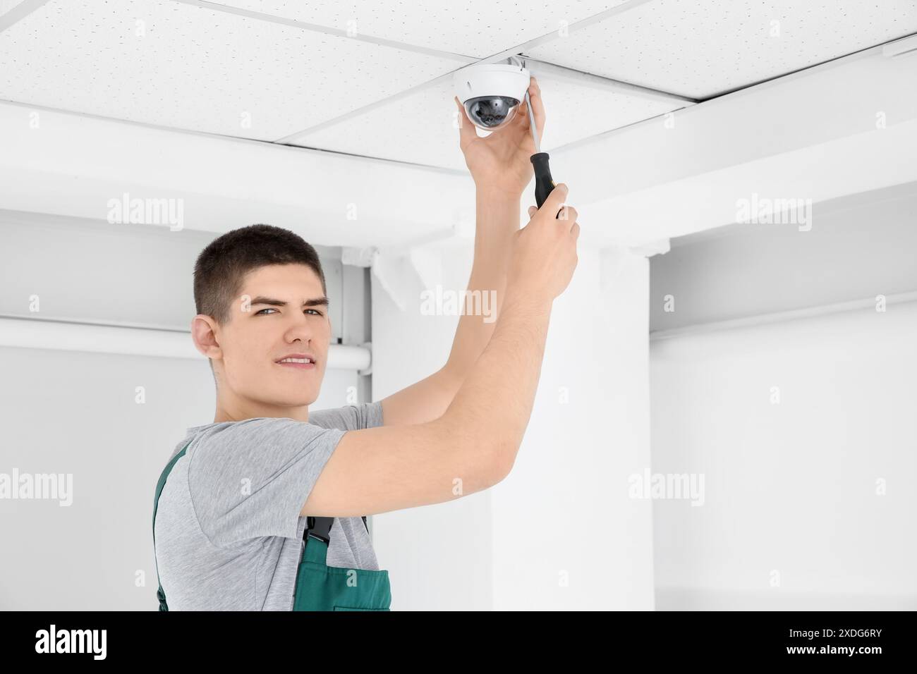 Technician with screwdriver installing CCTV camera on ceiling indoors ...