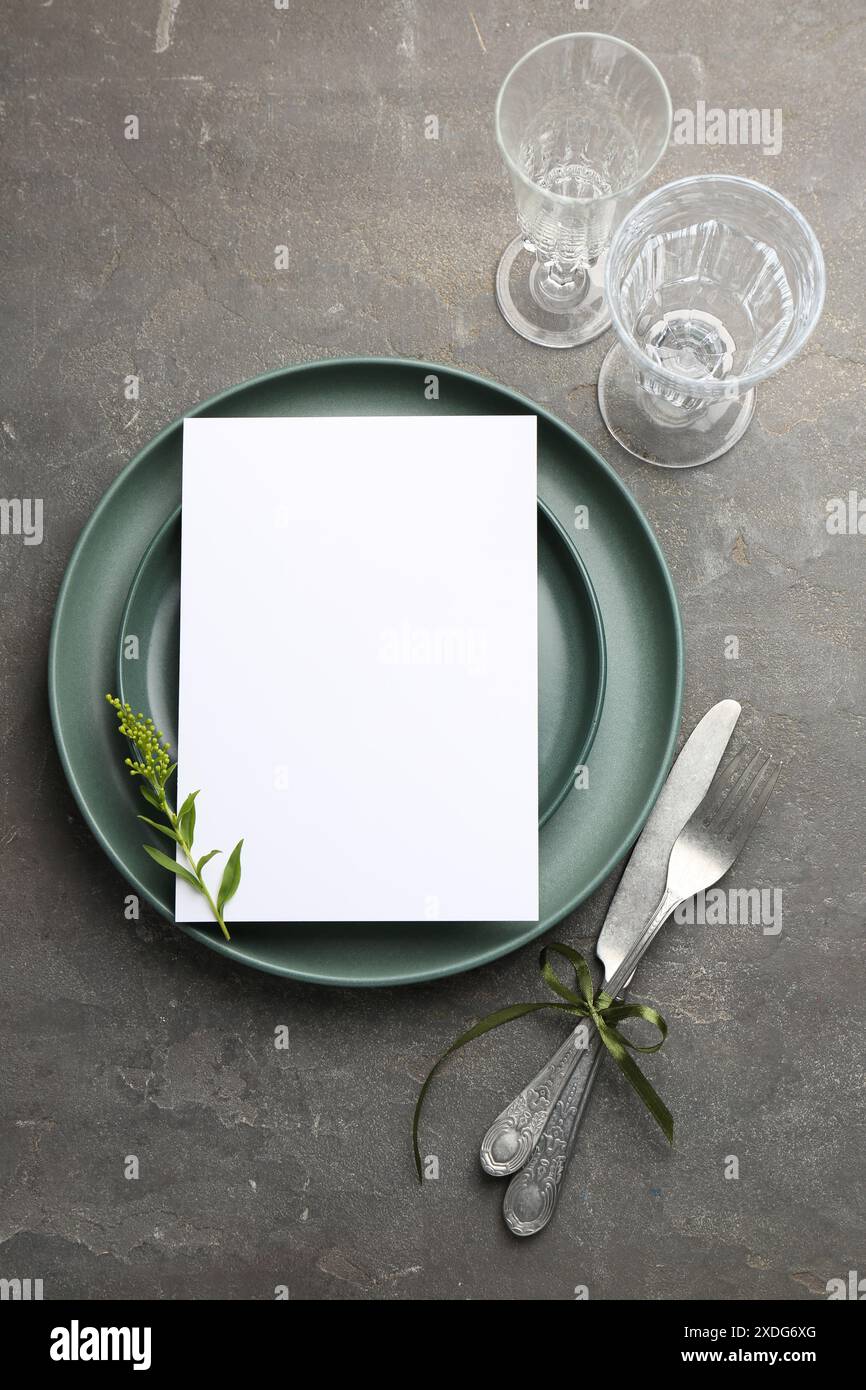 Empty menu, plates, cutlery, glasses and floral decor on grey table ...