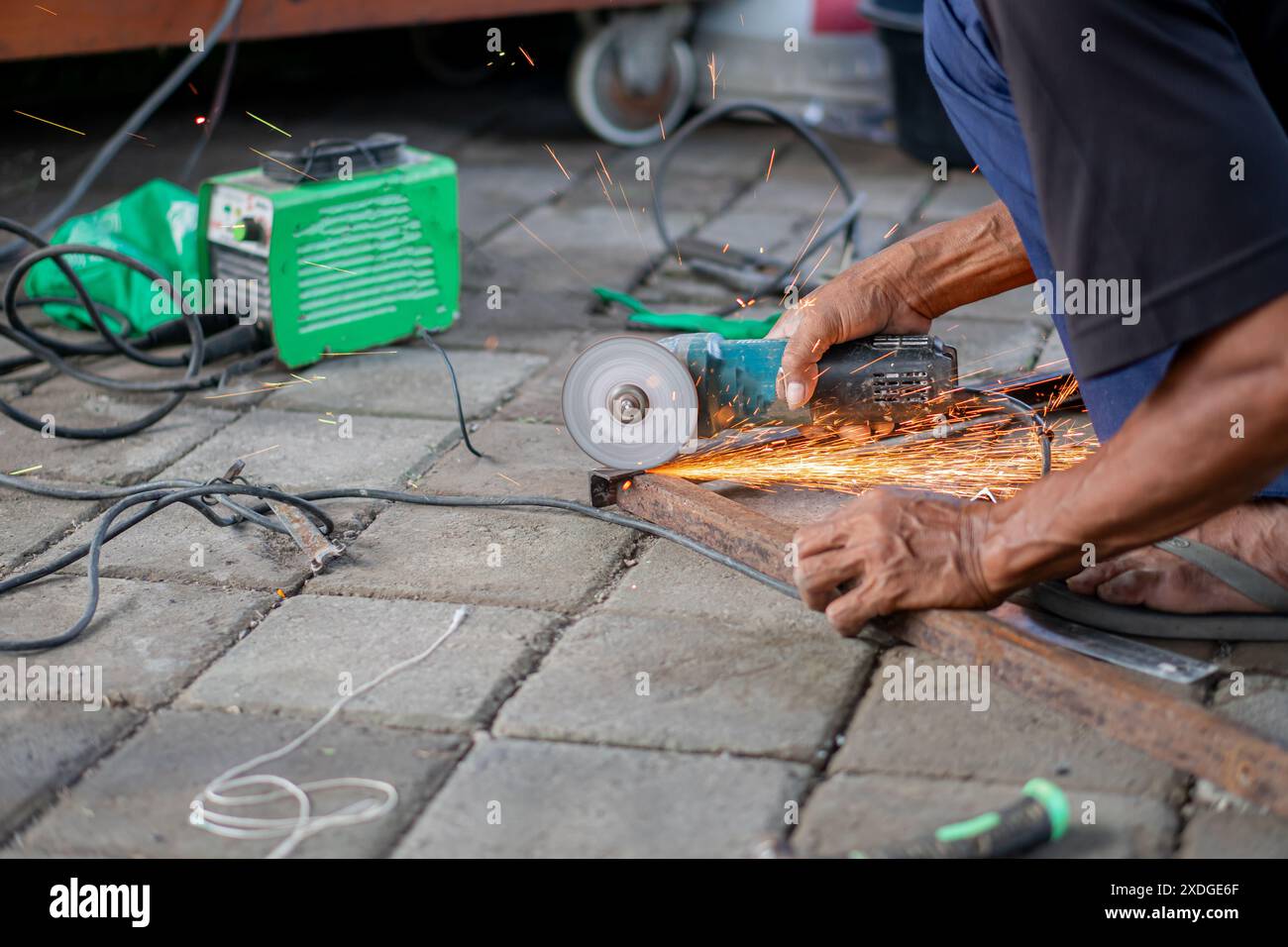 A person using an angle grinder to cut a metal piece, with sparks ...