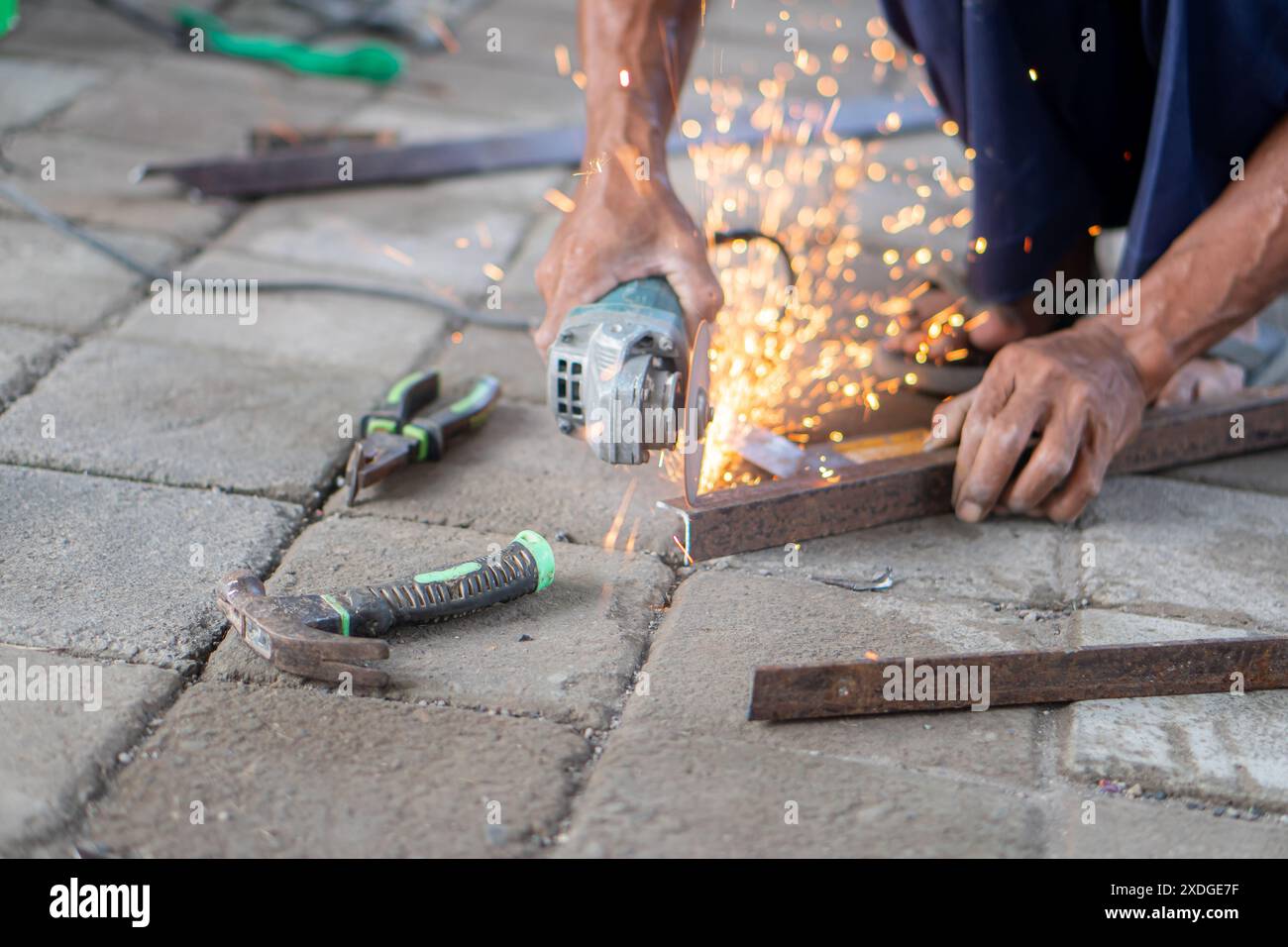 A person using an angle grinder to cut metal bars on a paved surface ...