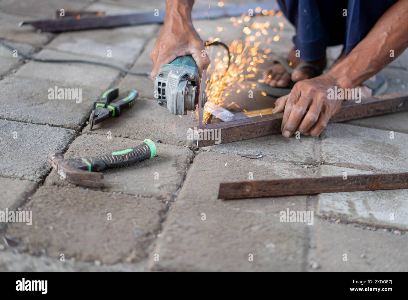A person using an angle grinder to cut metal bars on a paved surface ...
