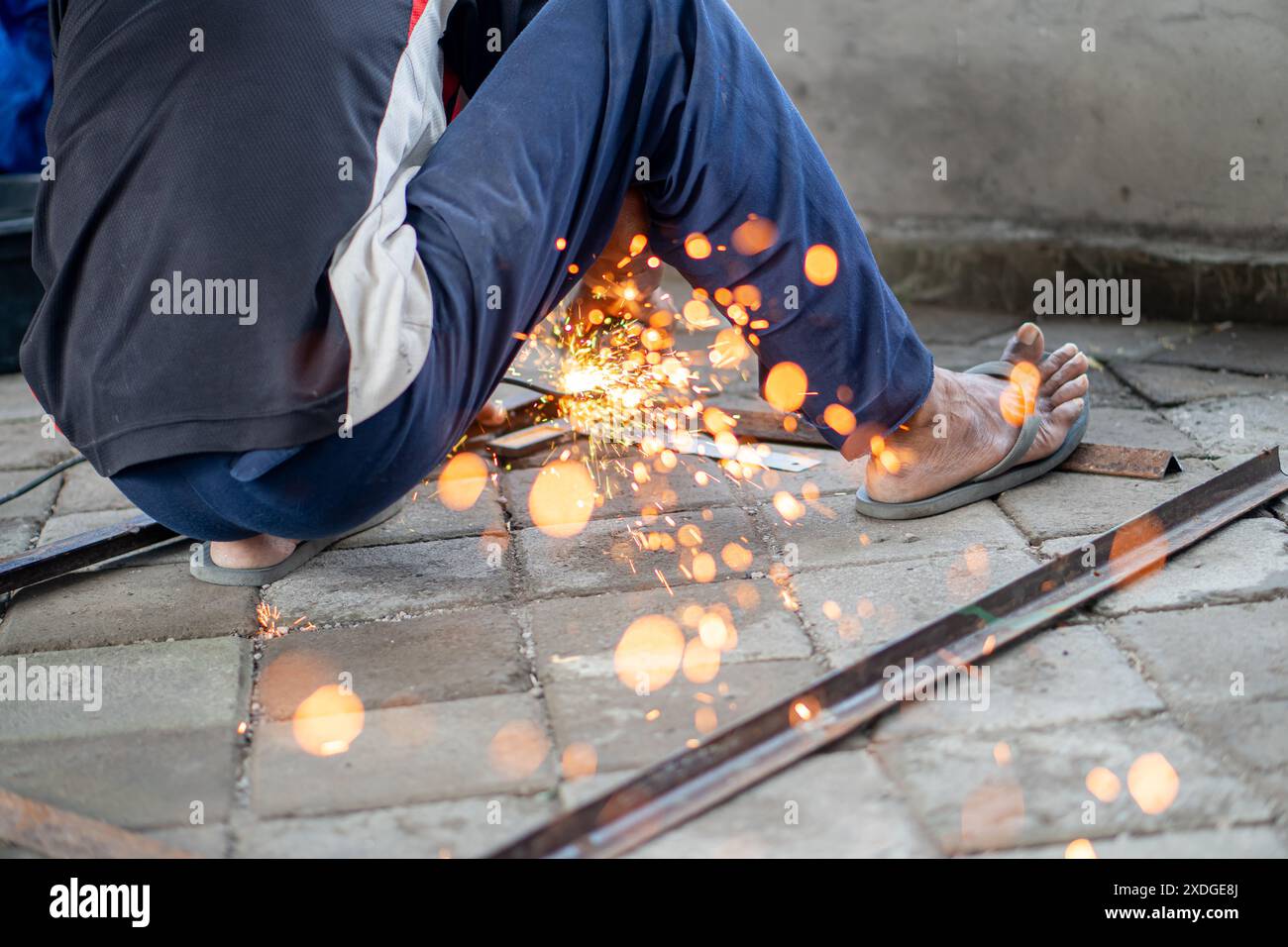 A person wearing flip-flops is welding metal pieces on a tiled floor ...
