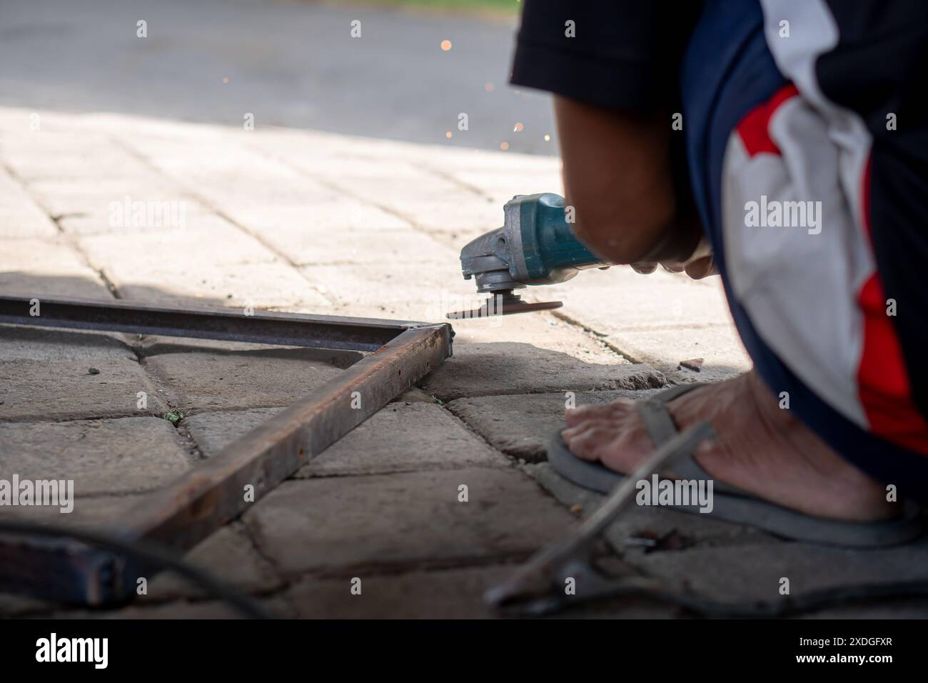 A person using an angle grinder to cut a metal frame on a paved surface ...